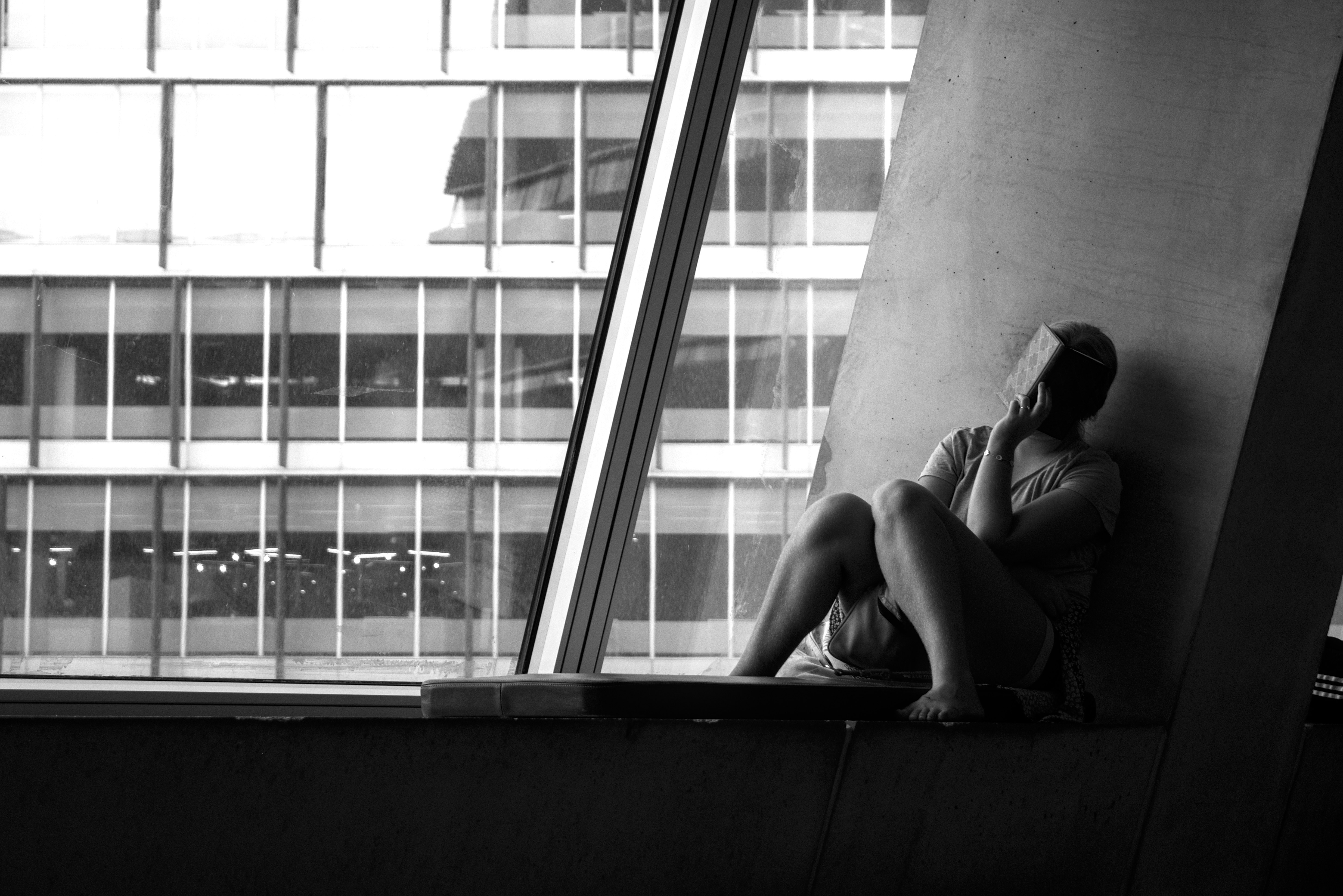 A girl reading sitted near a window | A woman sitting on a ledge next to a window