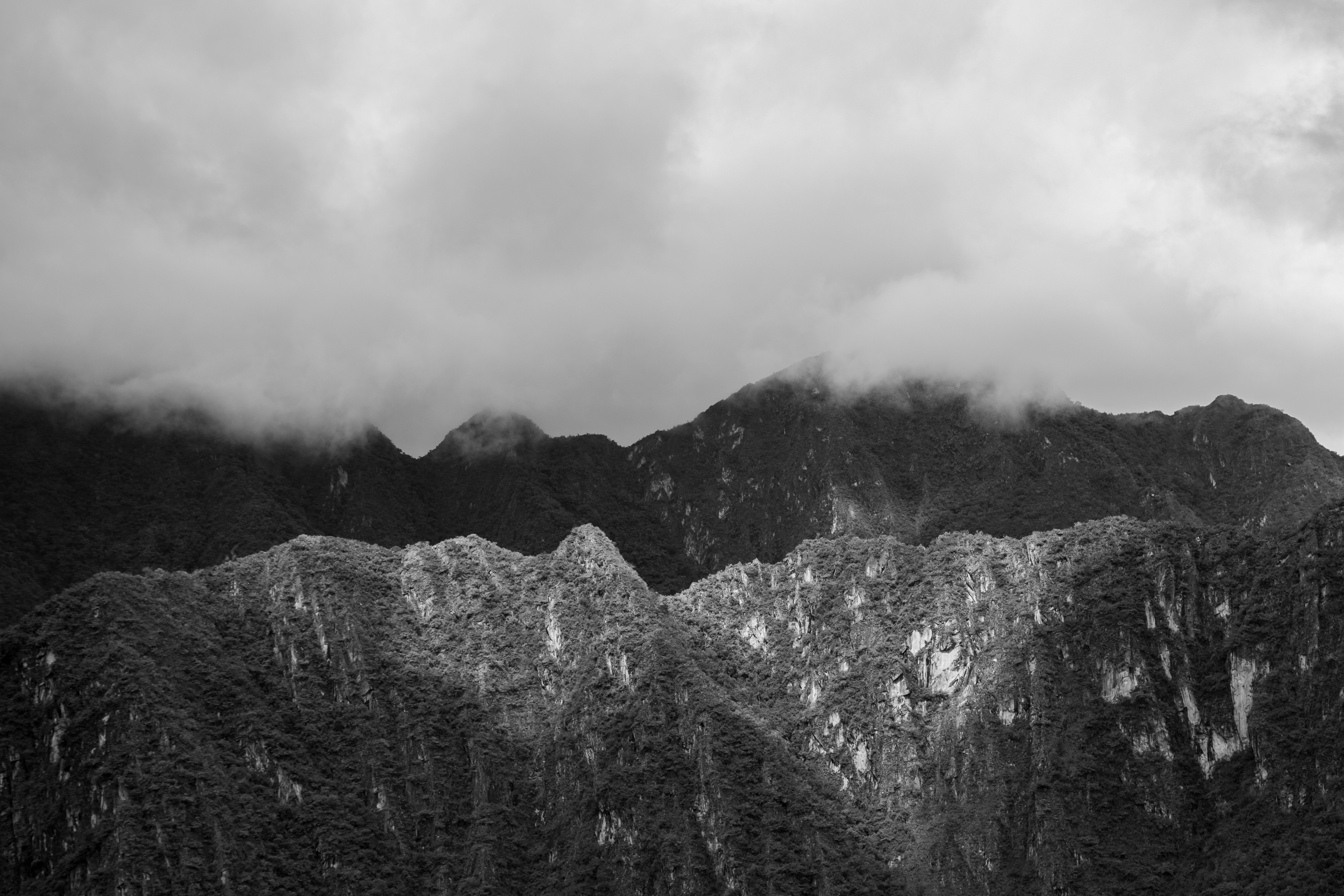 Mountain range shrouded in clouds with contrasting textures in grayscale.