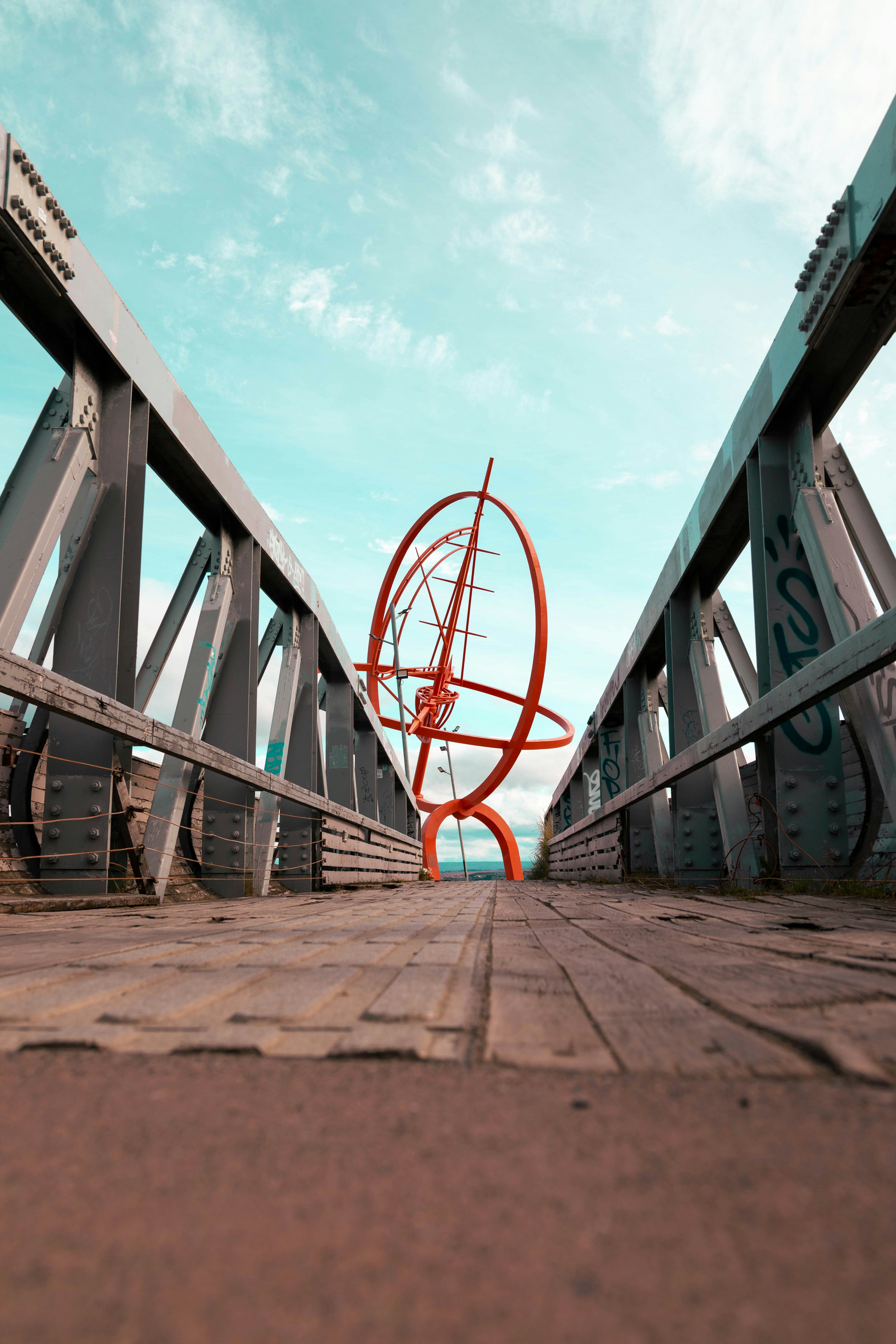 Between Rails and Ring: A Low-Angle Portrait of a Red Sculpture on the Bridge
