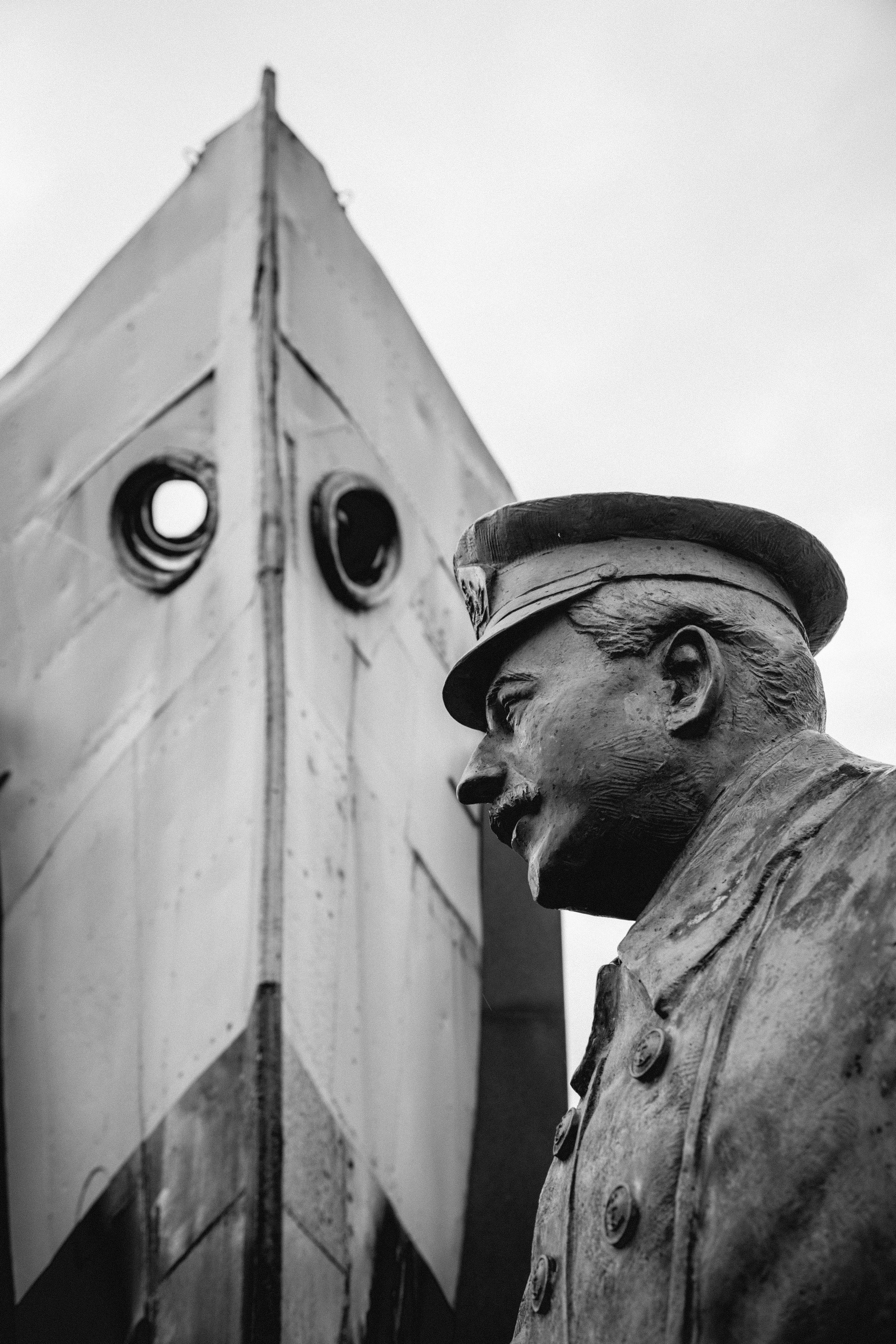 Maritime Sentinel: A Silent Sailor Stands Before a Weathered Vessel