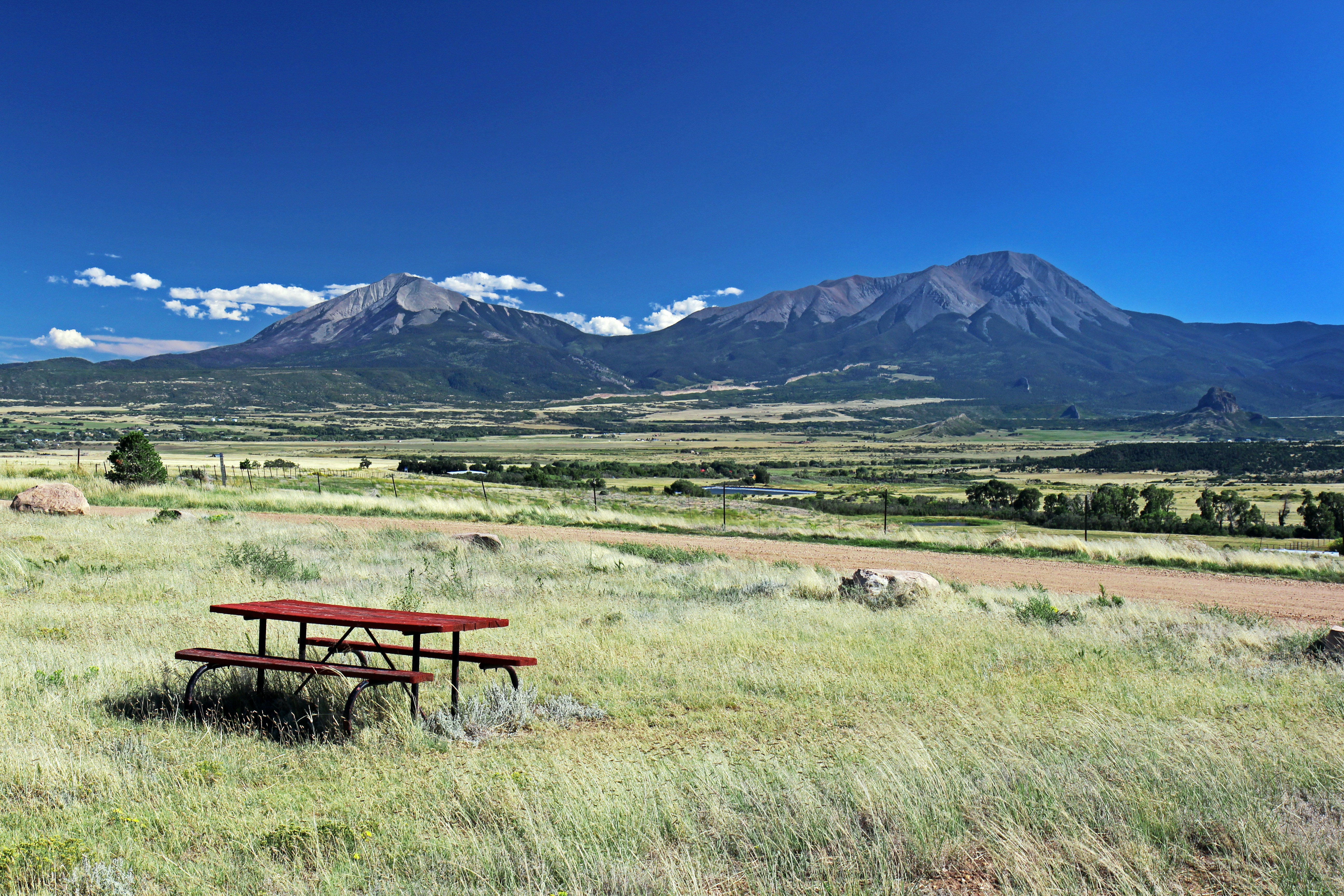 Red Picnic Table Anchors a Quiet Prairie Under Alpine Peaks