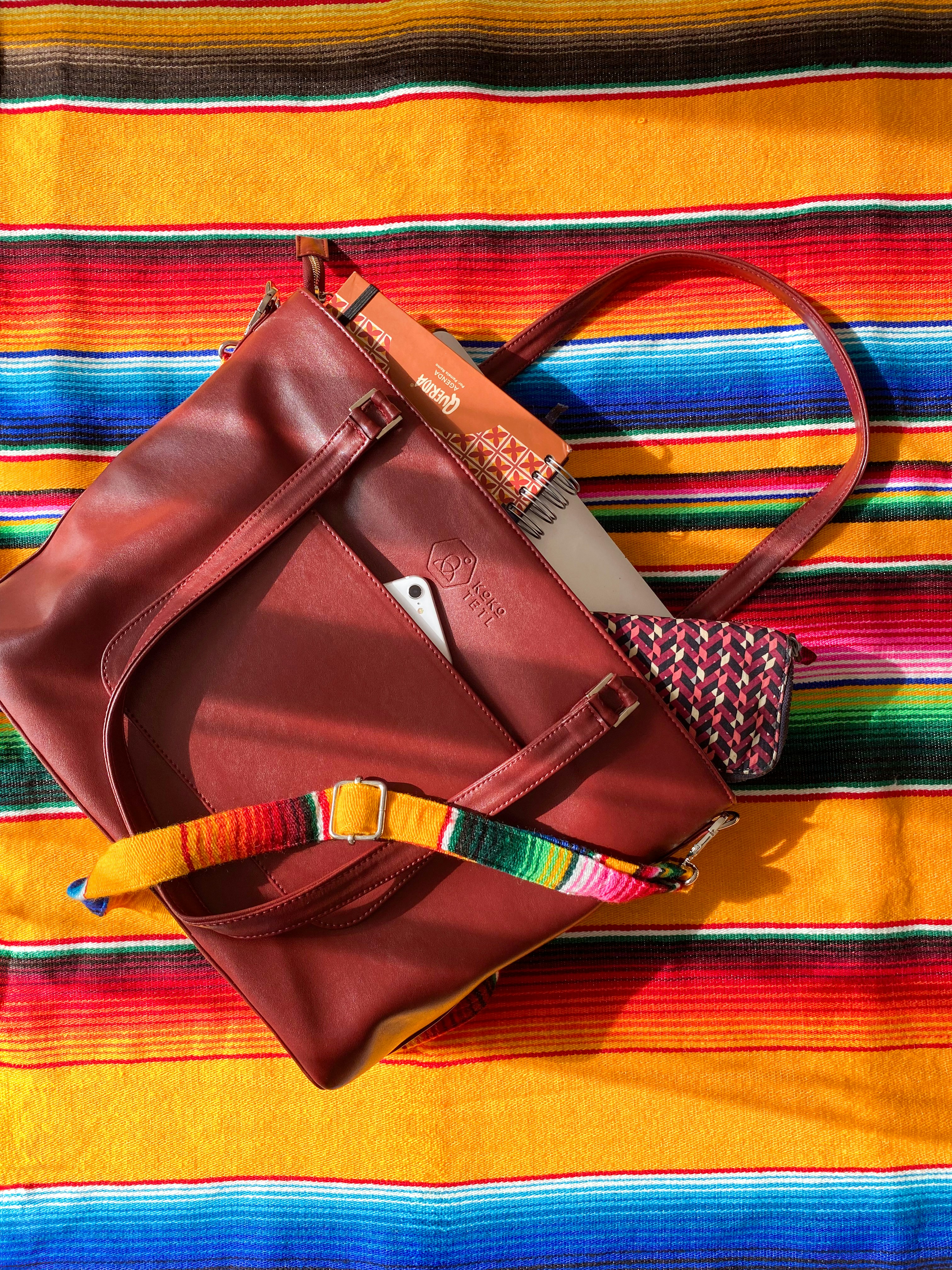 Burgundy leather tote resting on a sunlit rainbow-weave tapestry