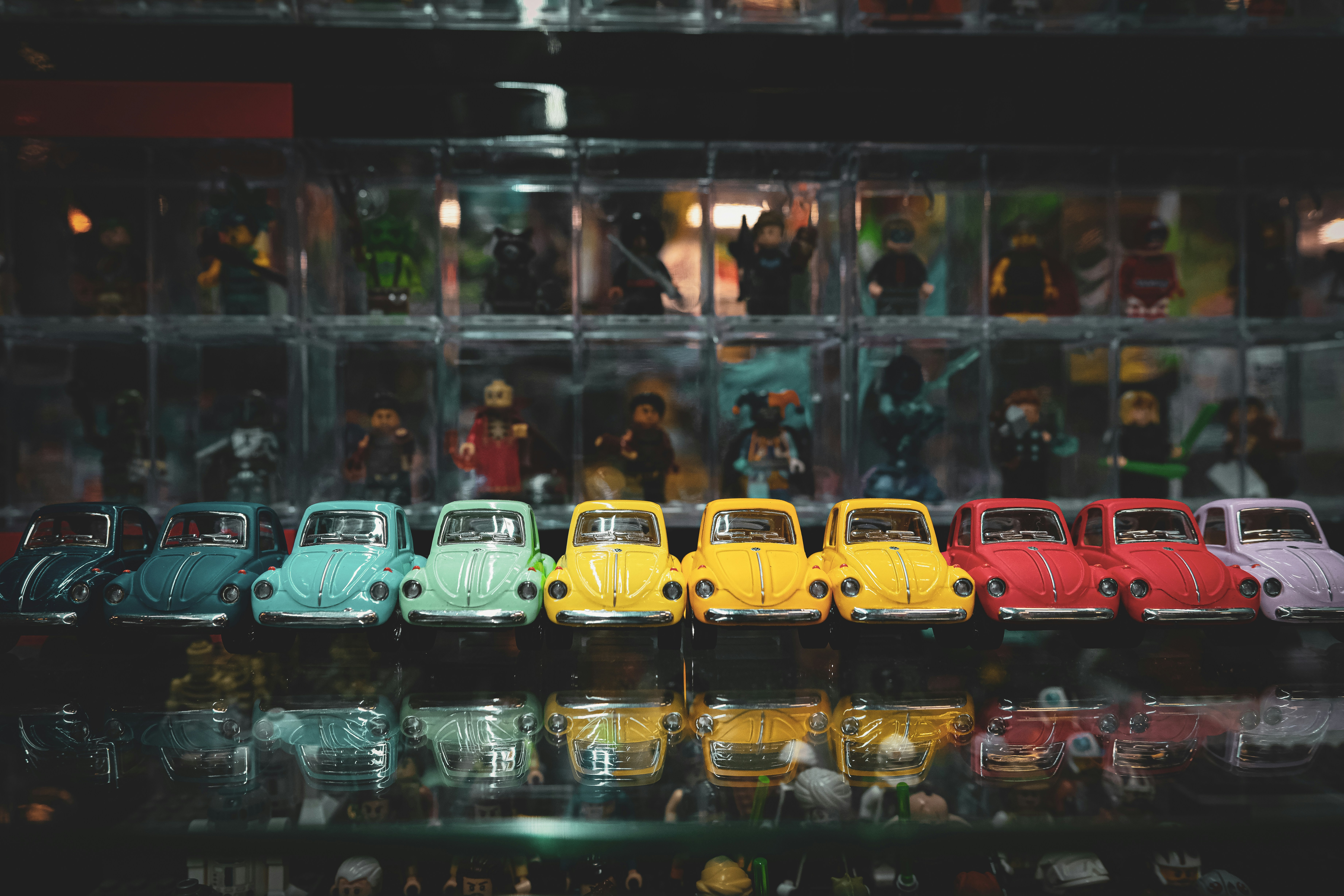 Row of colorful toy cars displayed on a reflective surface under dim lighting.