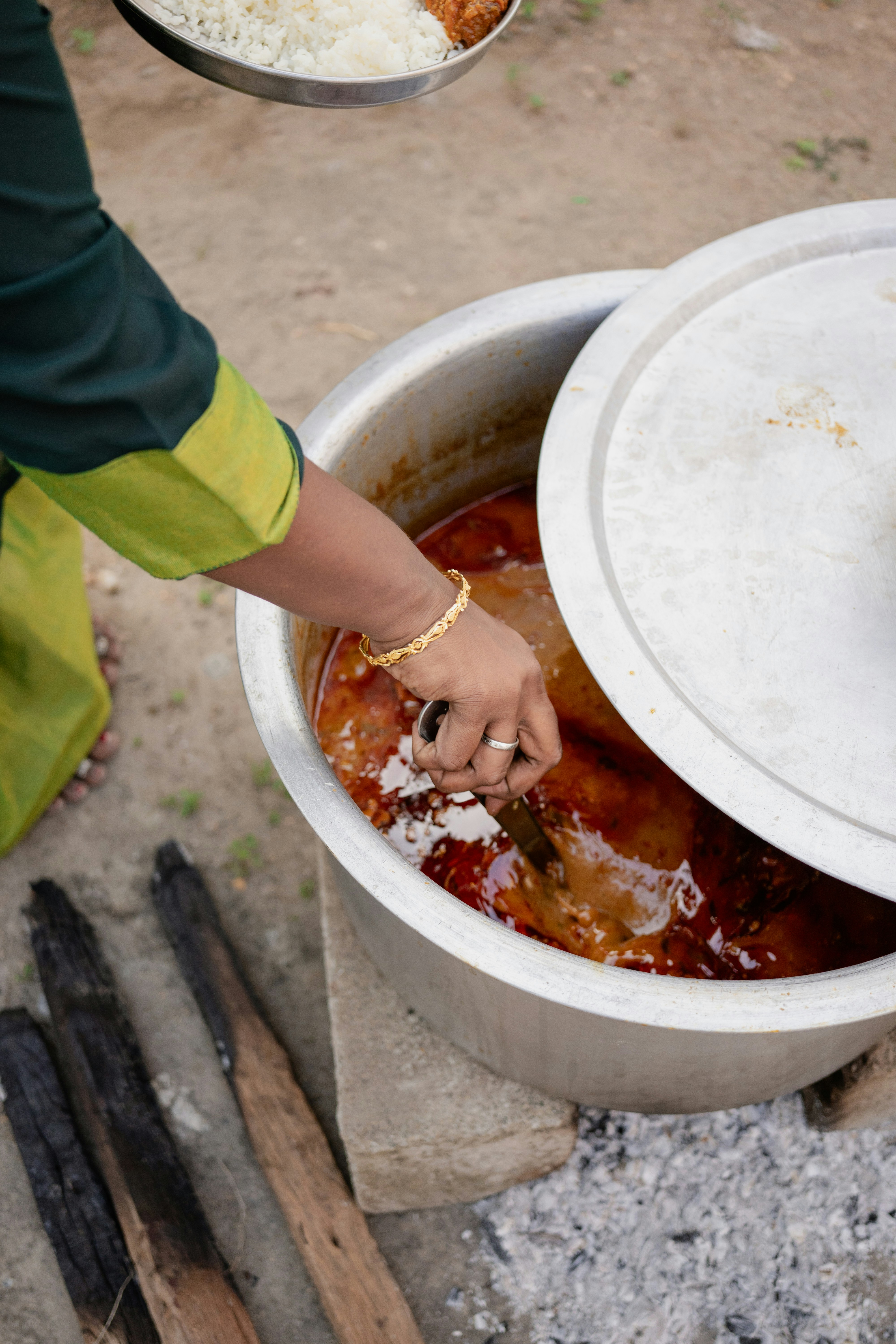 Outdoor Curry Alchemy: Hand Stirring a Rich Red Sauce in a Steel Pot