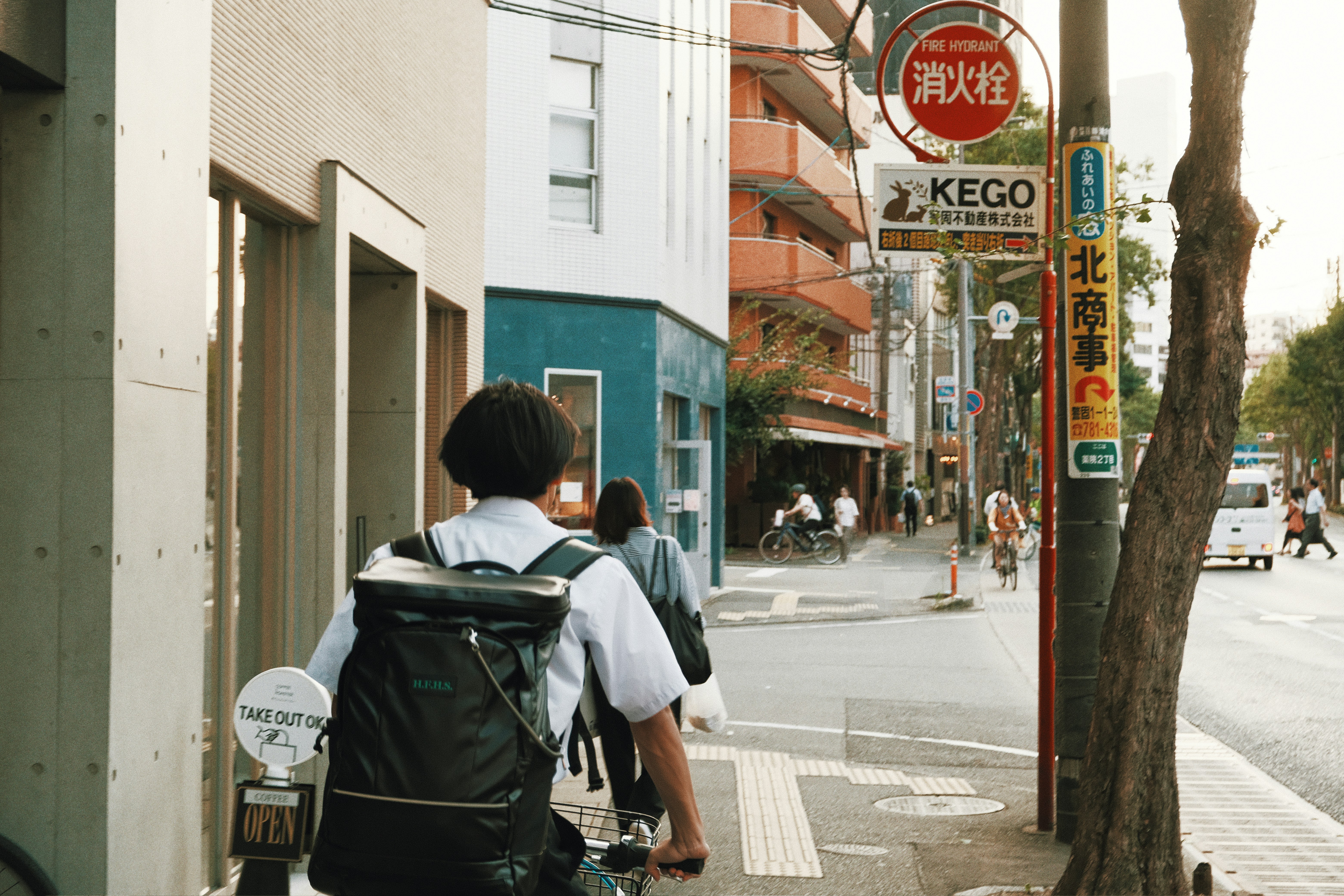 Cyclist navigating a lively city street lined with colorful storefronts and signs under warm afternoon light.