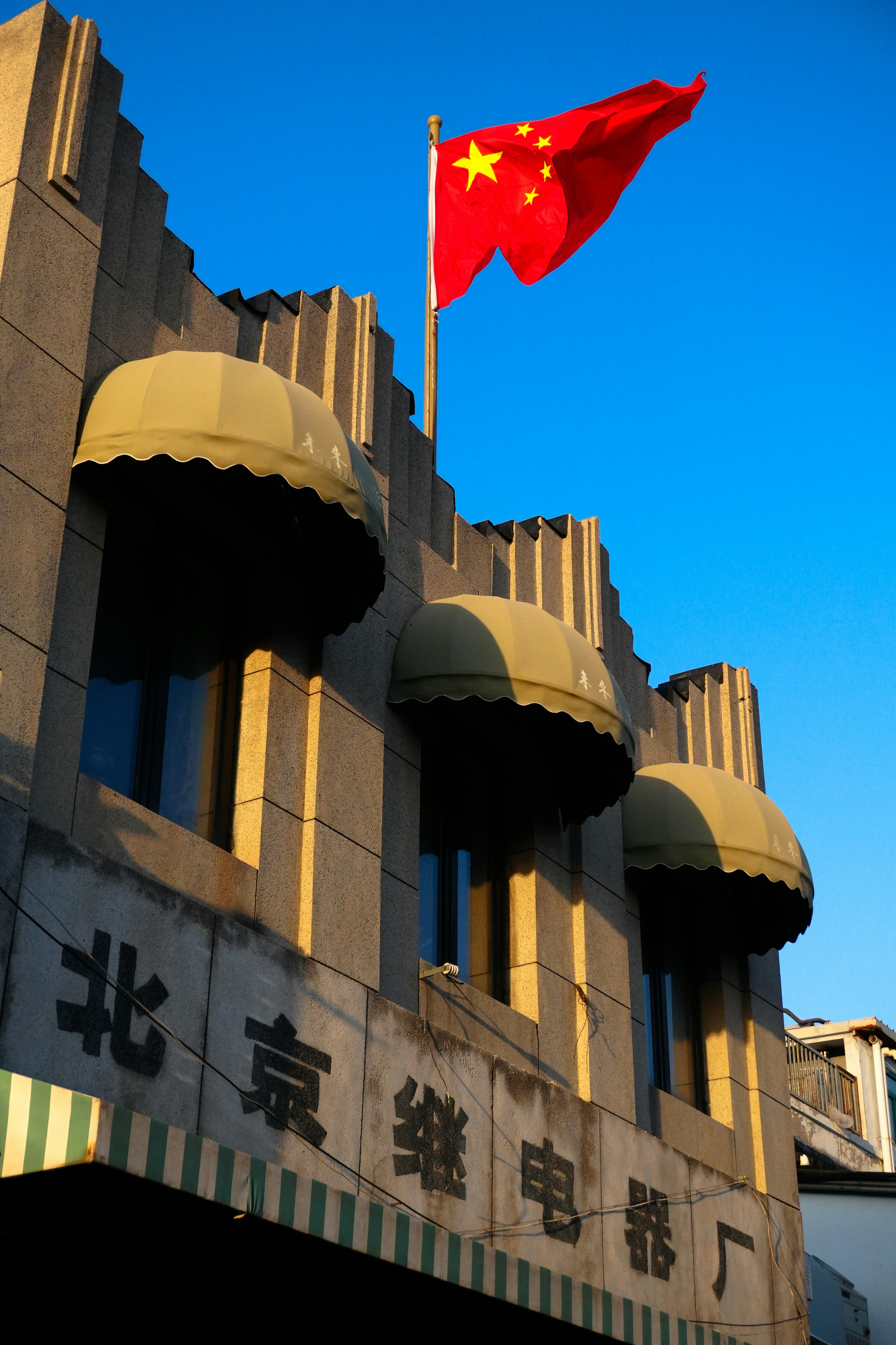 Historic building facade with green awnings and a Chinese flag against a vibrant blue sky.