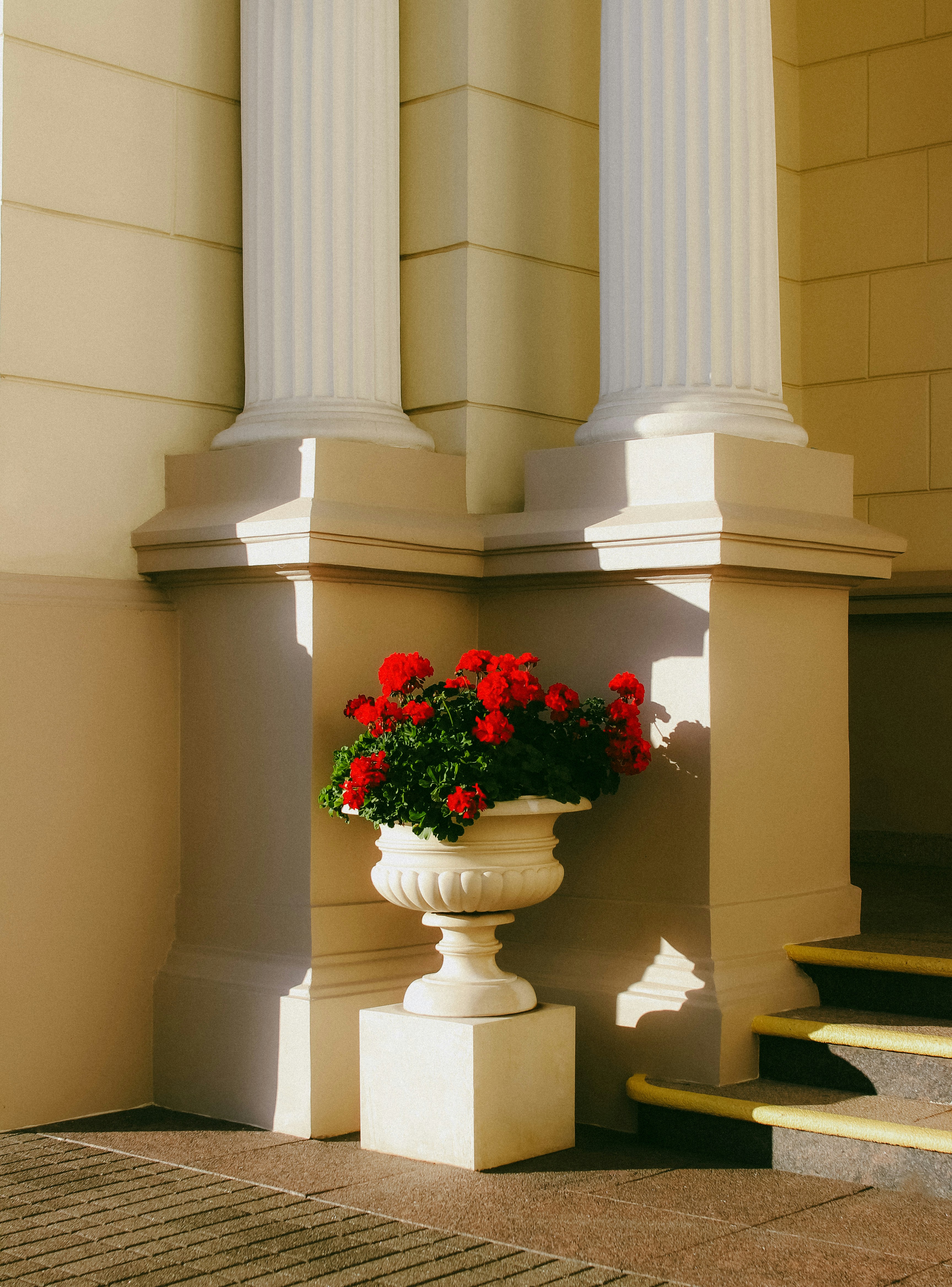 A white vase with red flowers sitting on the side of a building