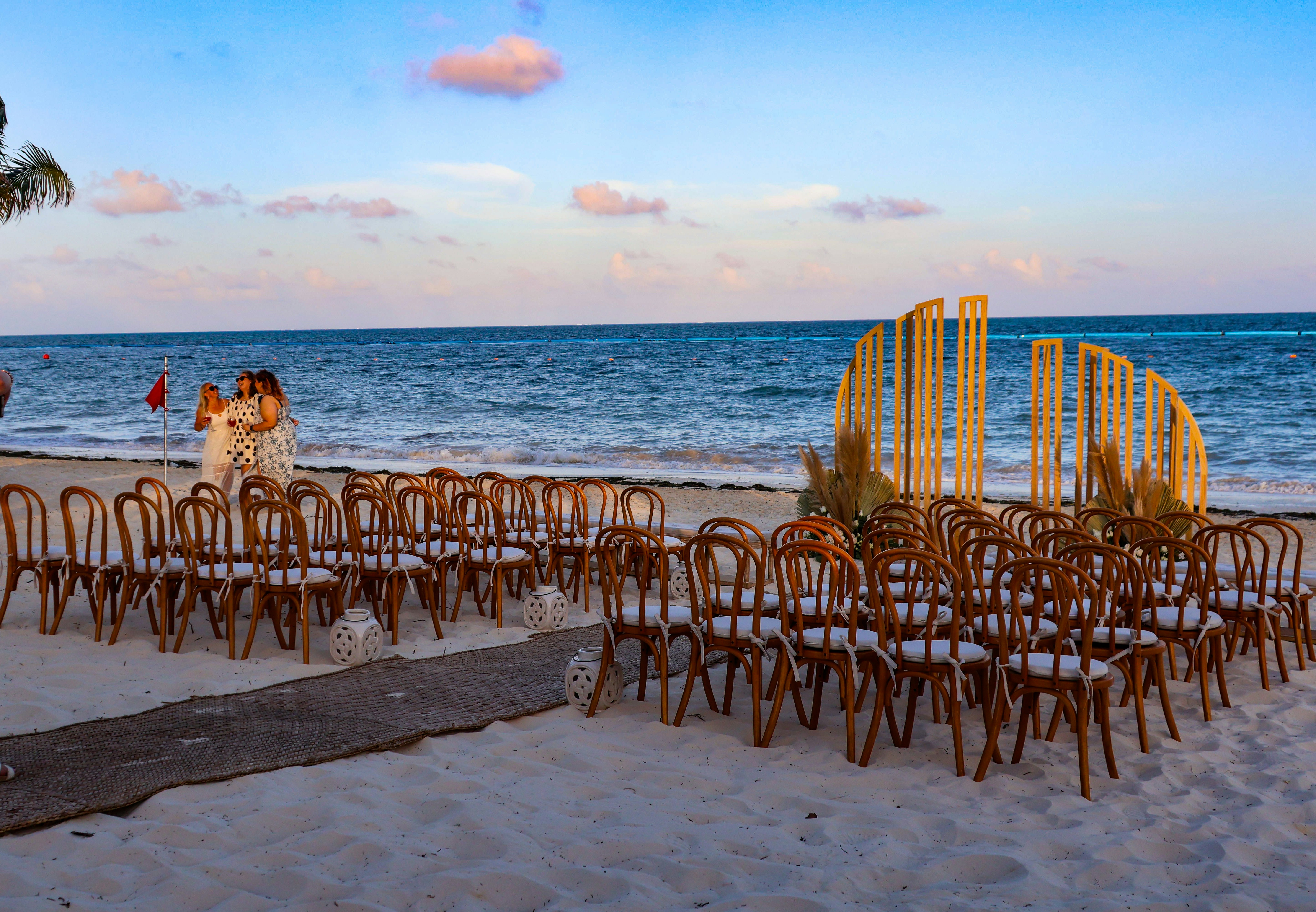Rows of chairs facing a minimalist arch on a sandy beach under a vibrant blue sky.