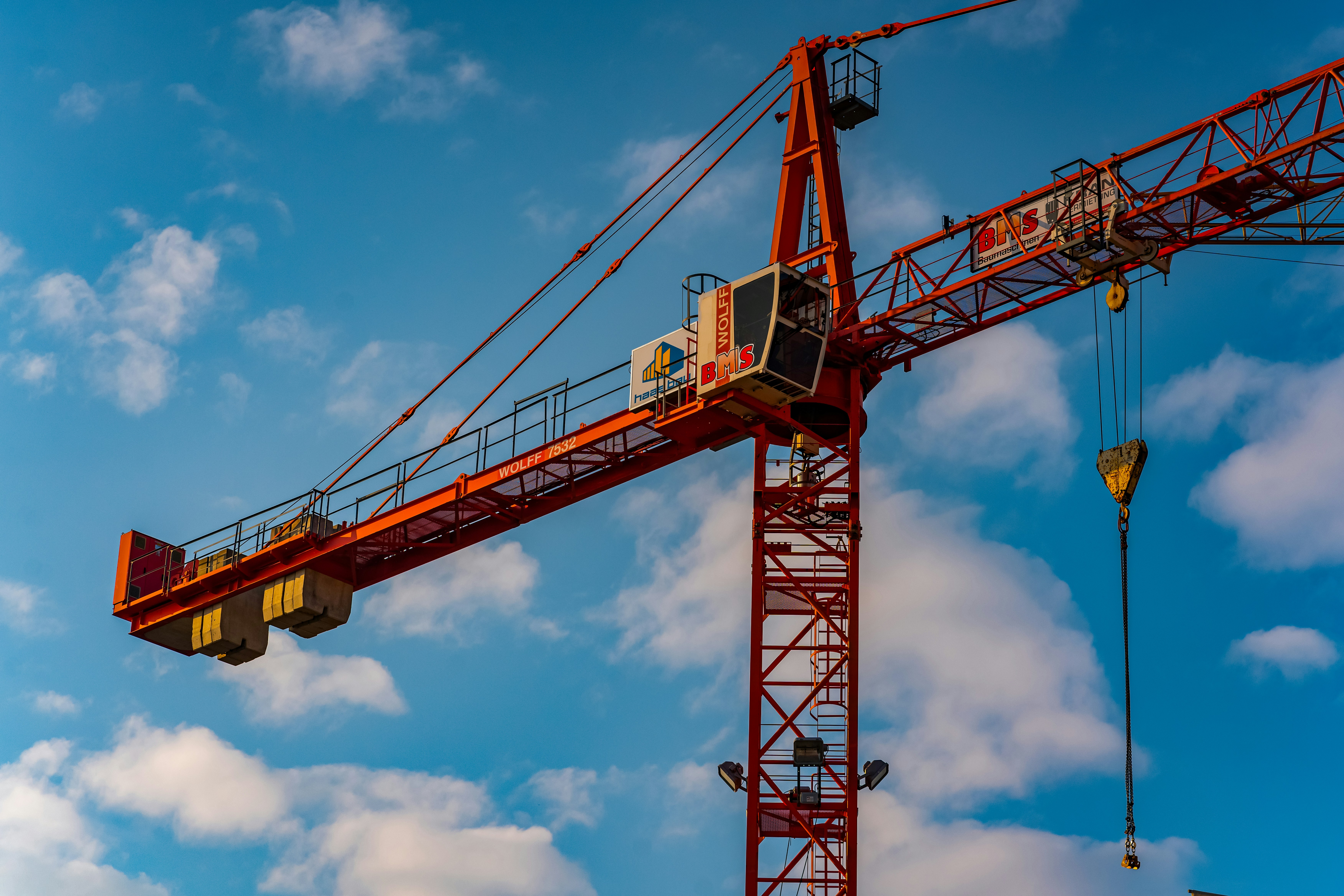 Red construction crane silhouetted against a blue sky with scattered clouds, highlighting its industrial strength and progress.
