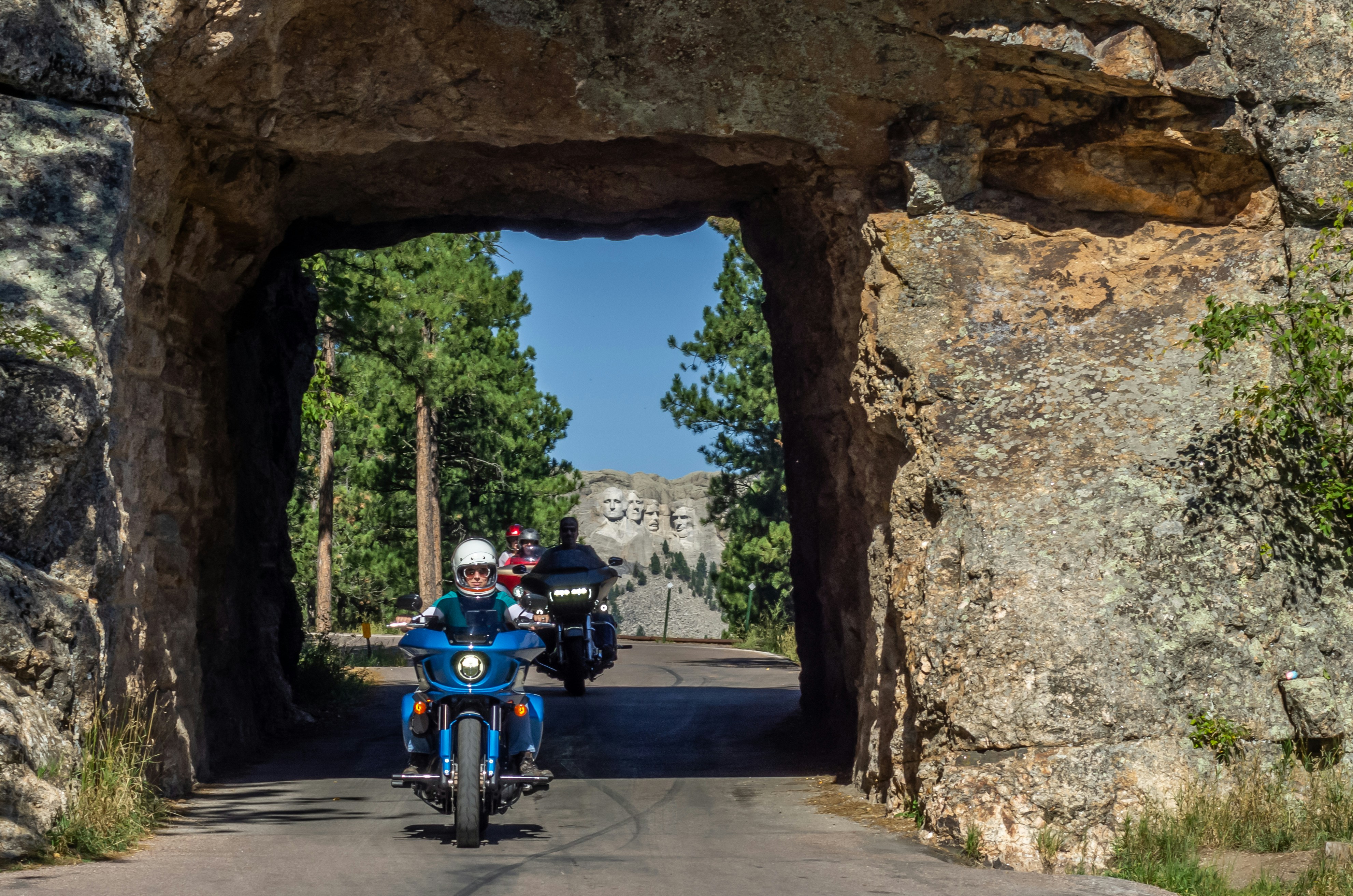 Riders Emerging Through a Stone Arch into Sunlit Forest Road