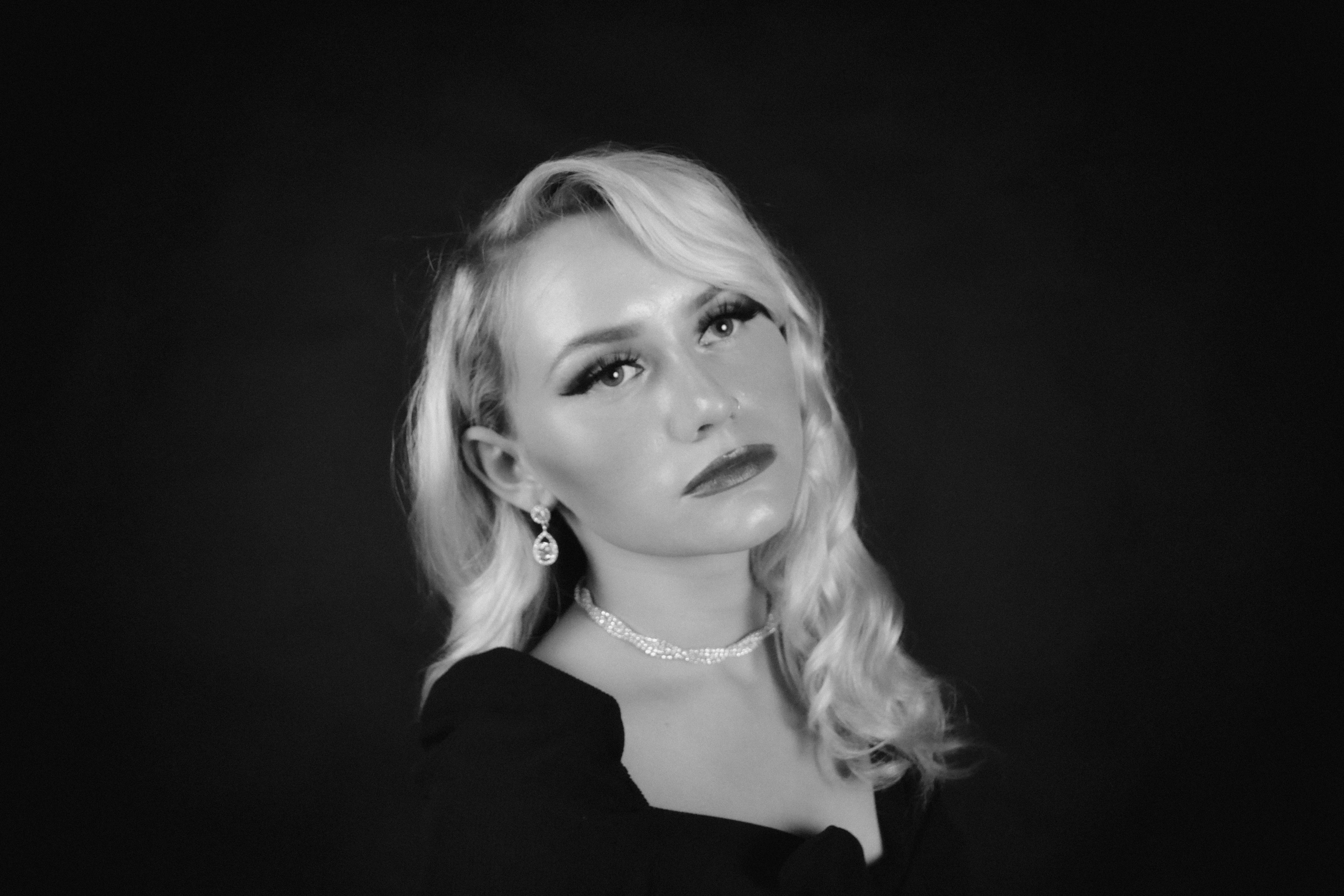 Woman with elegant curls and jewelry in a high-contrast black and white portrait.