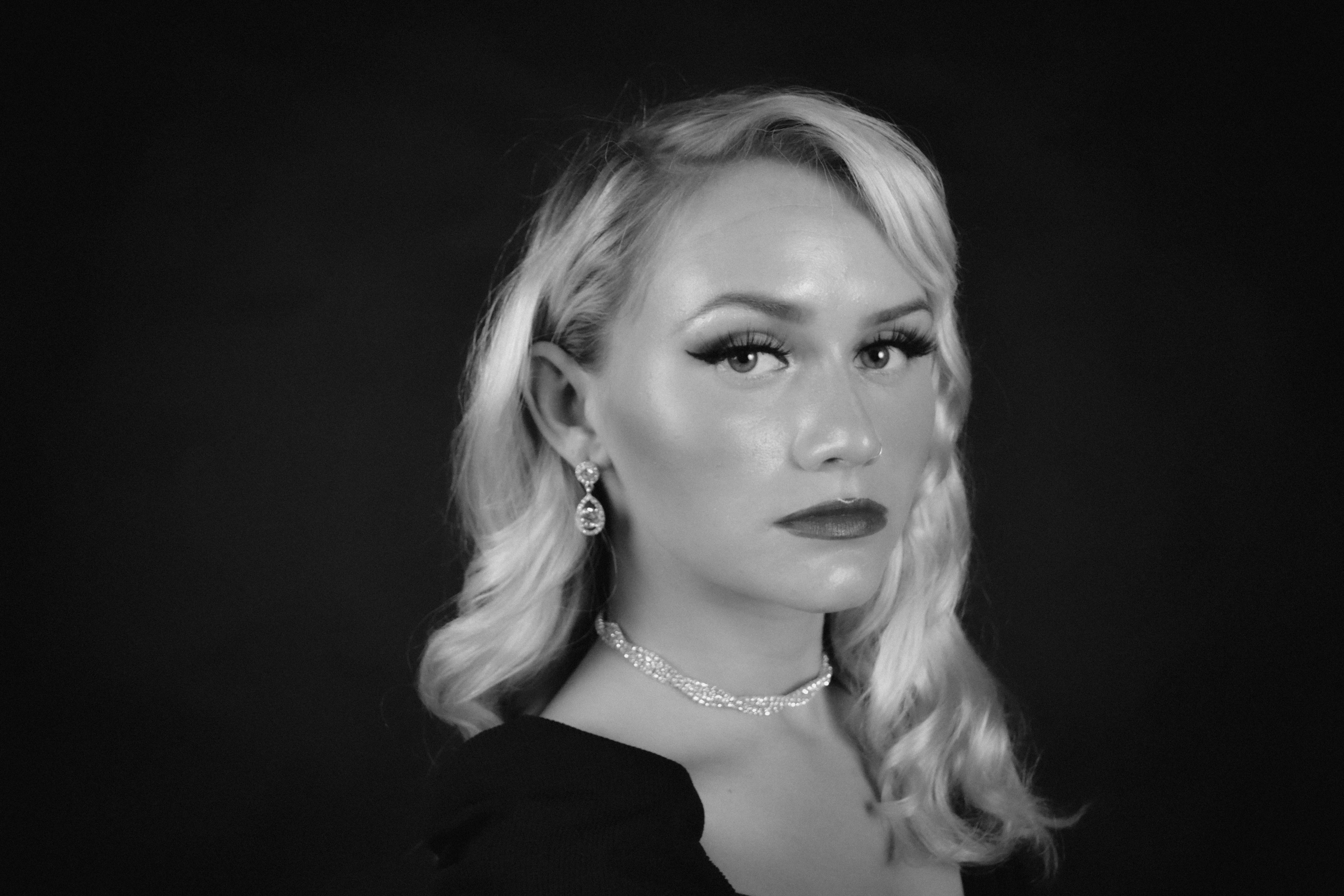 Black and white portrait of a woman with soft curls and elegant jewelry, her expression highlighted by dramatic lighting.