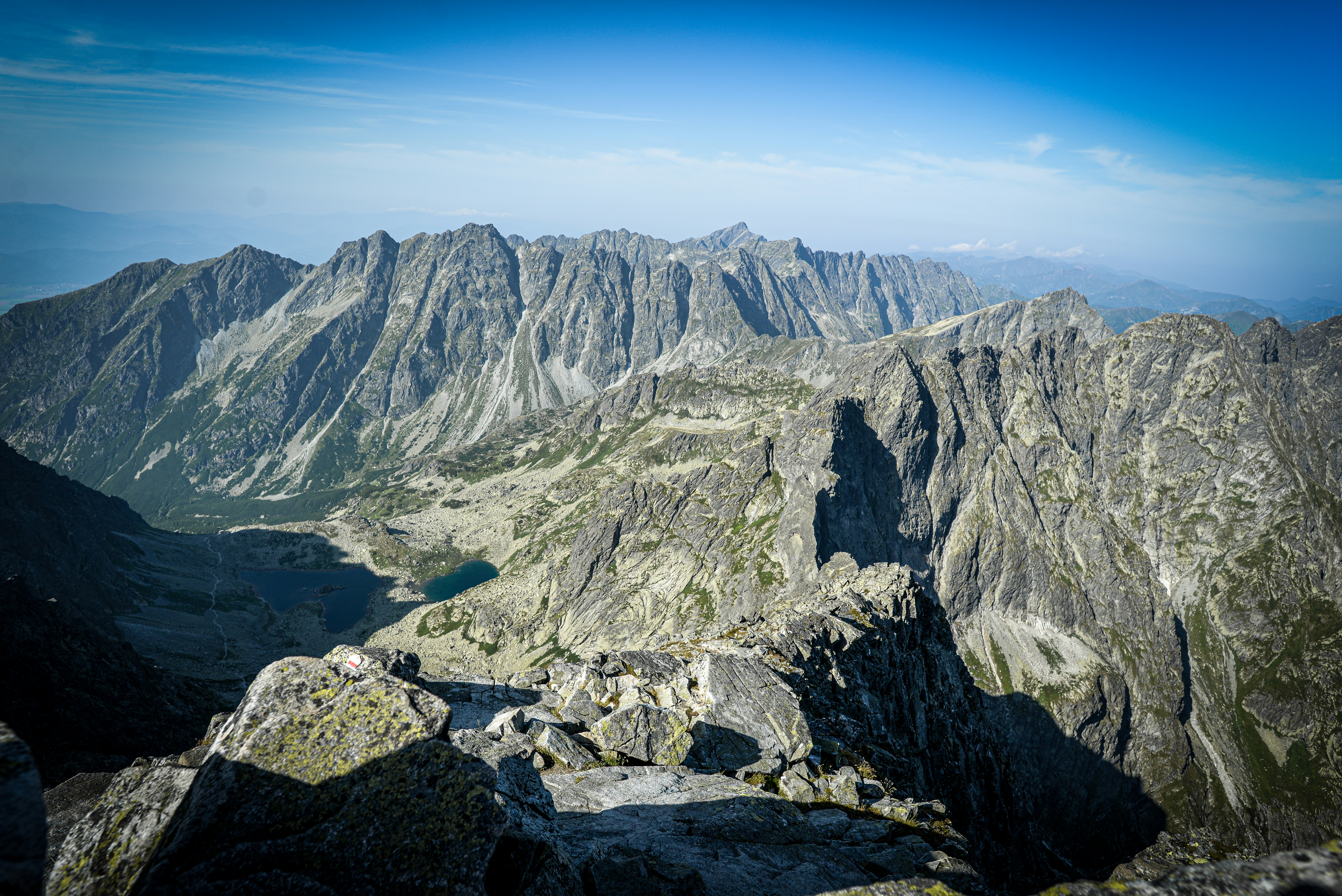 Rugged mountain peaks rise sharply under a vivid blue sky, contrasting with the rocky foreground and distant horizon.