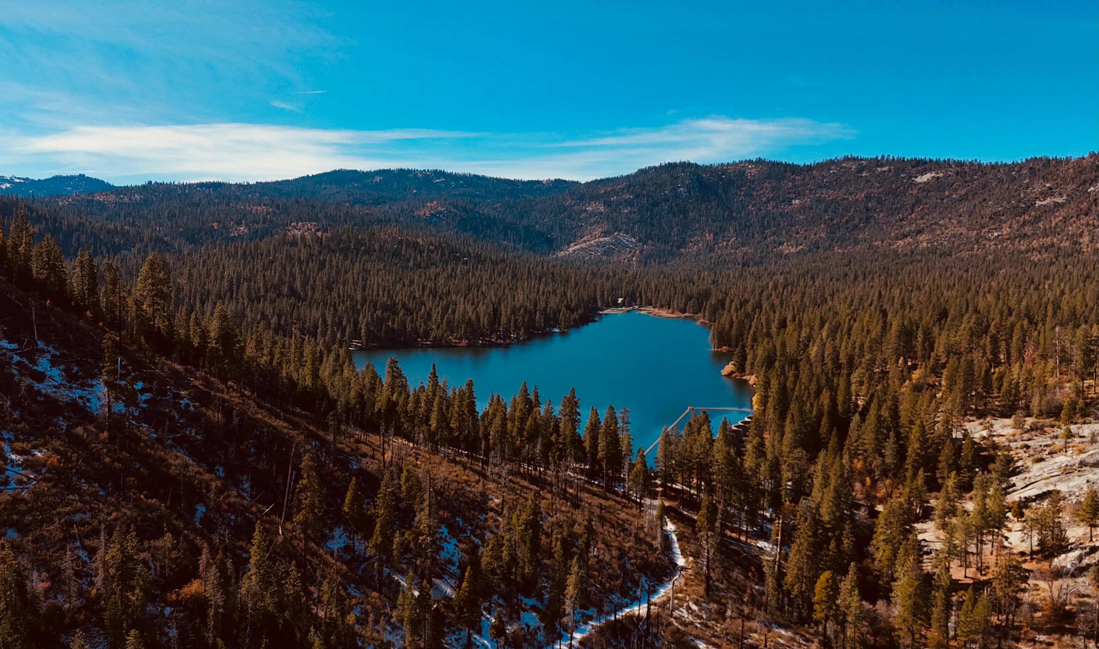 Serene mountain lake surrounded by dense evergreen forests under a clear blue sky.