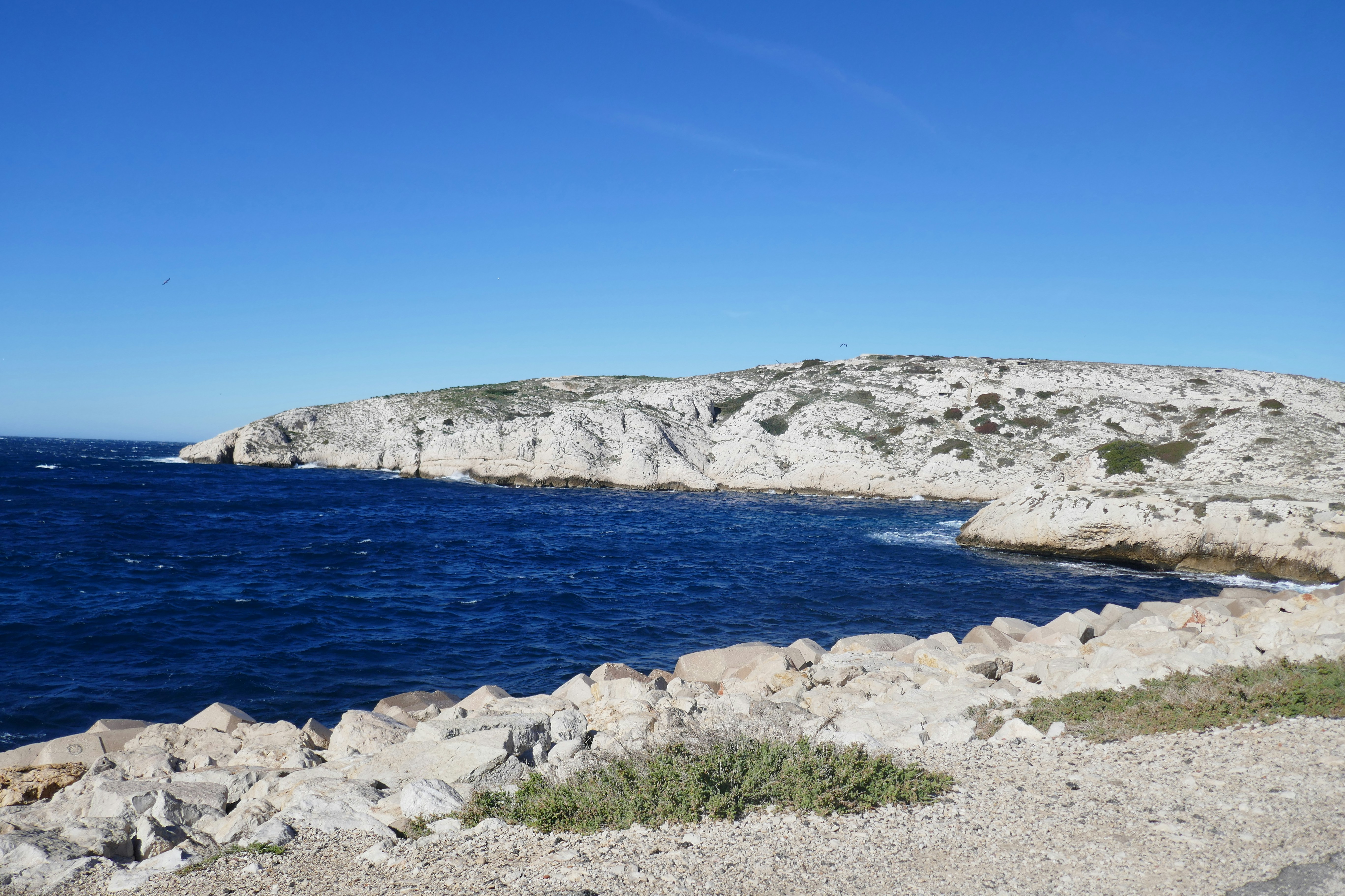Rocky shoreline with deep blue ocean and rugged cliffs under clear sky.