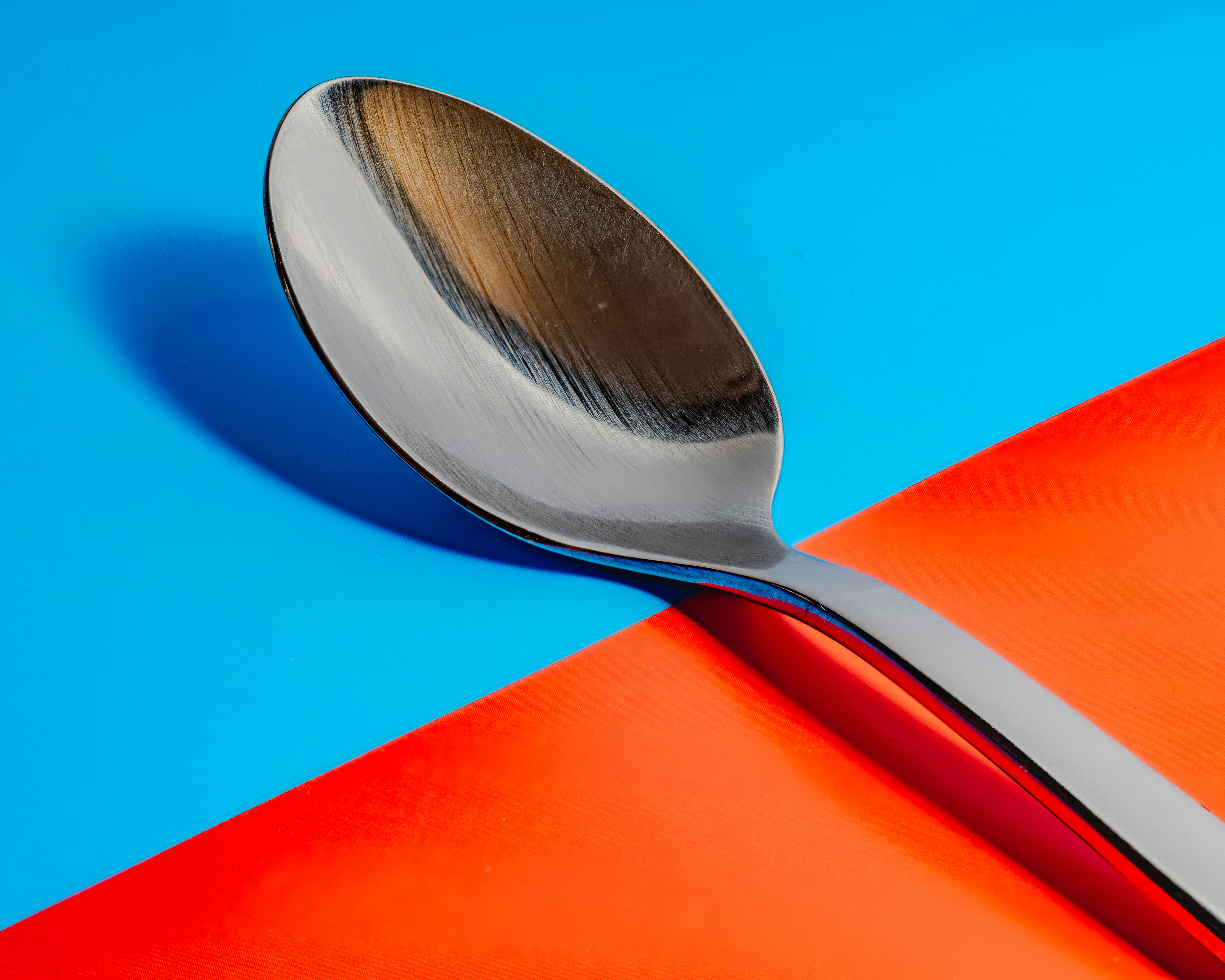 A silver spoon sitting on top of a red and blue surface photo – Free ...