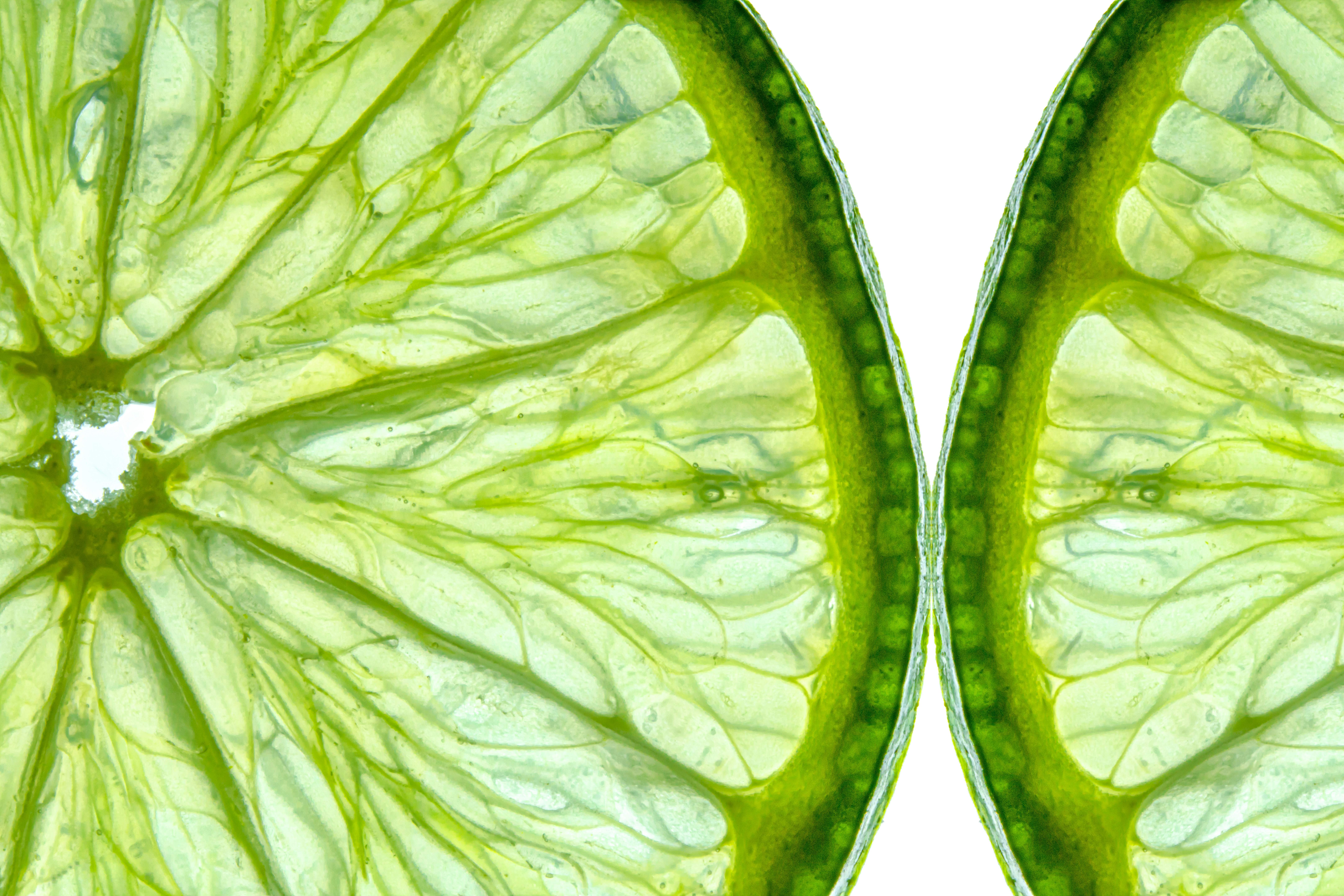 Close-up of lime slices arranged symmetrically against a white background, highlighting translucent green hues and detailed textures.