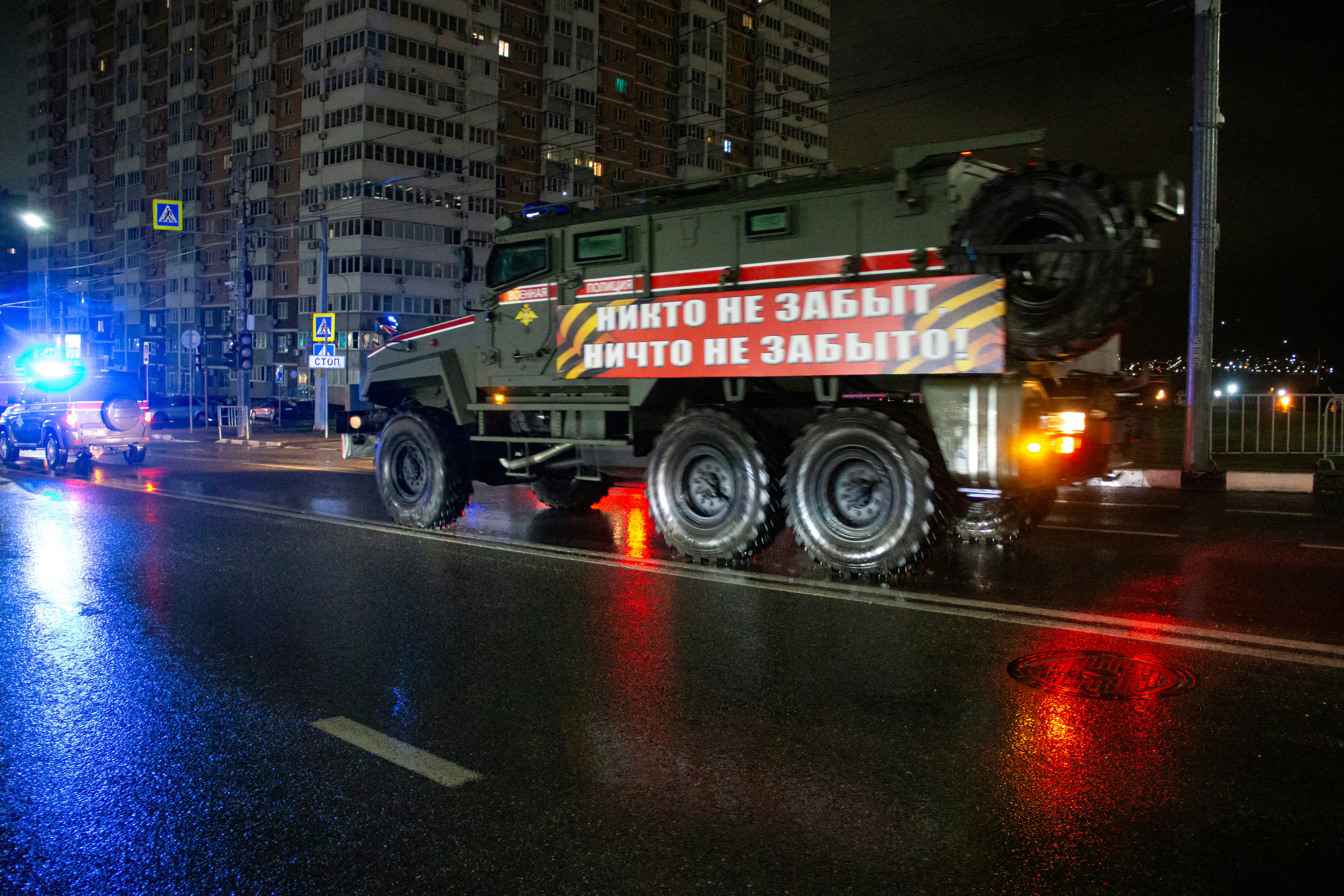 Nocturnal Banner: Memorial Armored Vehicle Rumbles Through a Rain-Slick City