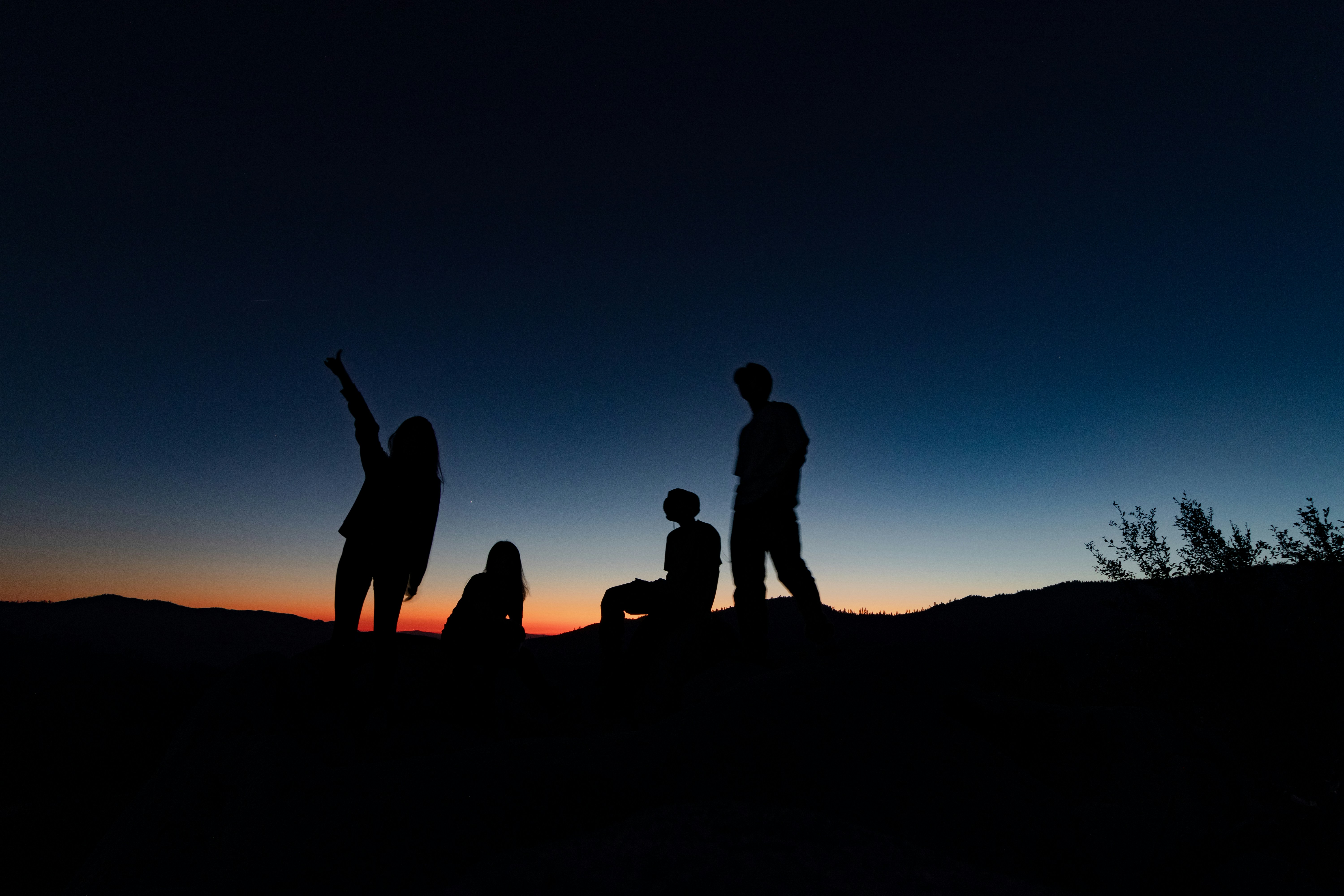 Silhouetted figures stand on a hilltop under a deepening blue and orange twilight sky.
