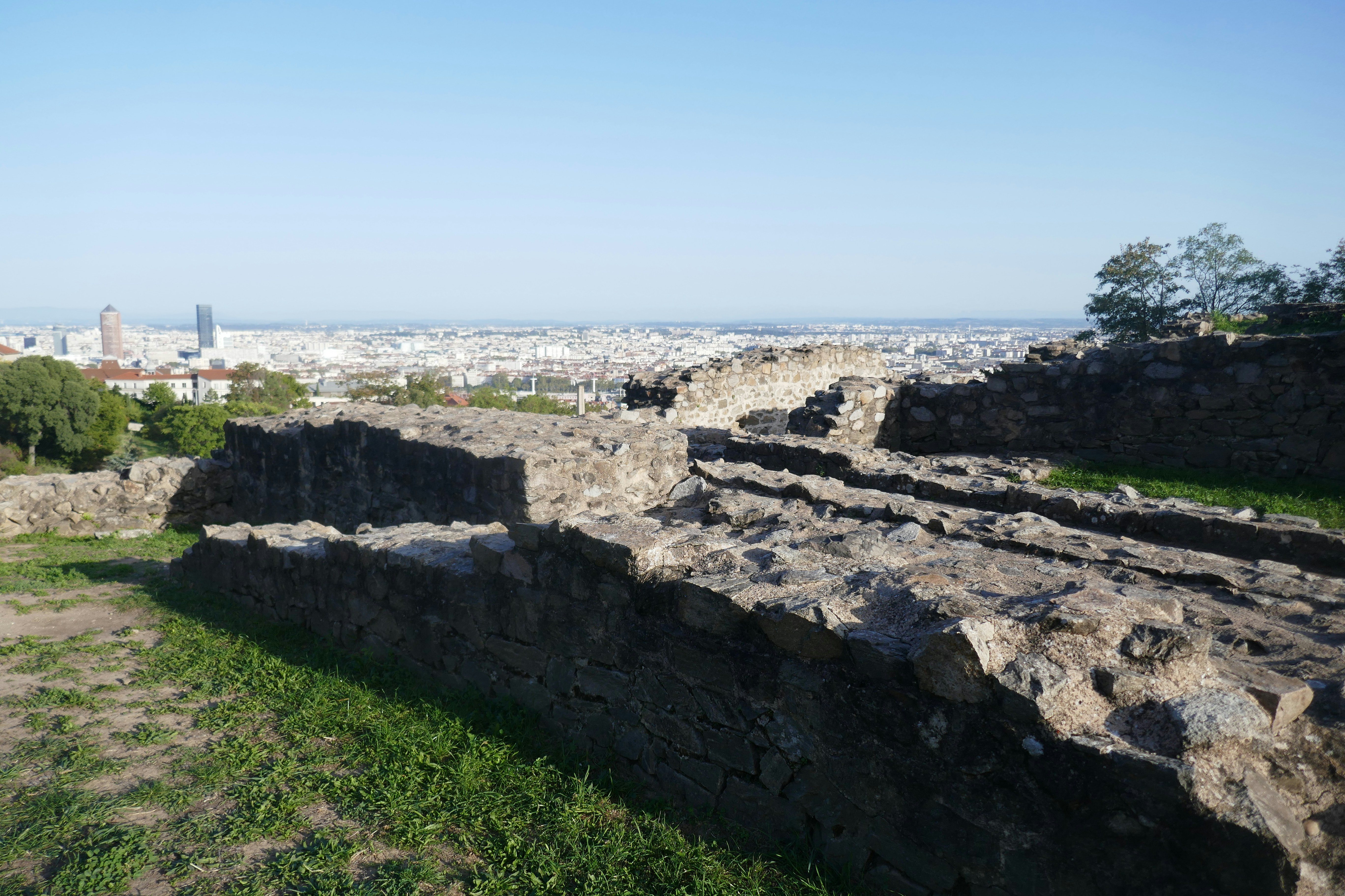 Stone ruins with a cityscape in the distance under a clear blue sky.