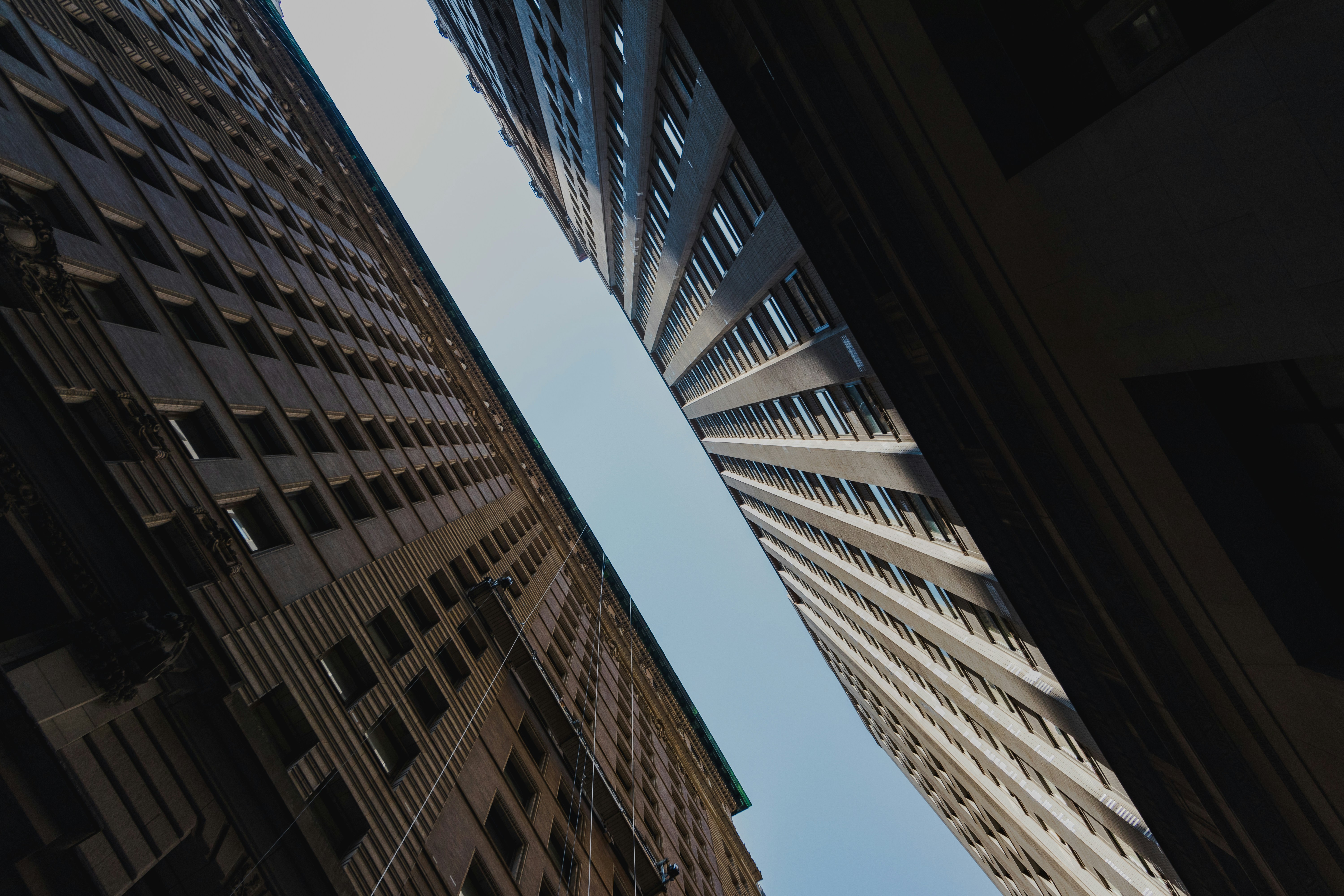 Skyward view between two skyscrapers forming a dramatic urban canyon against a clear blue sky.