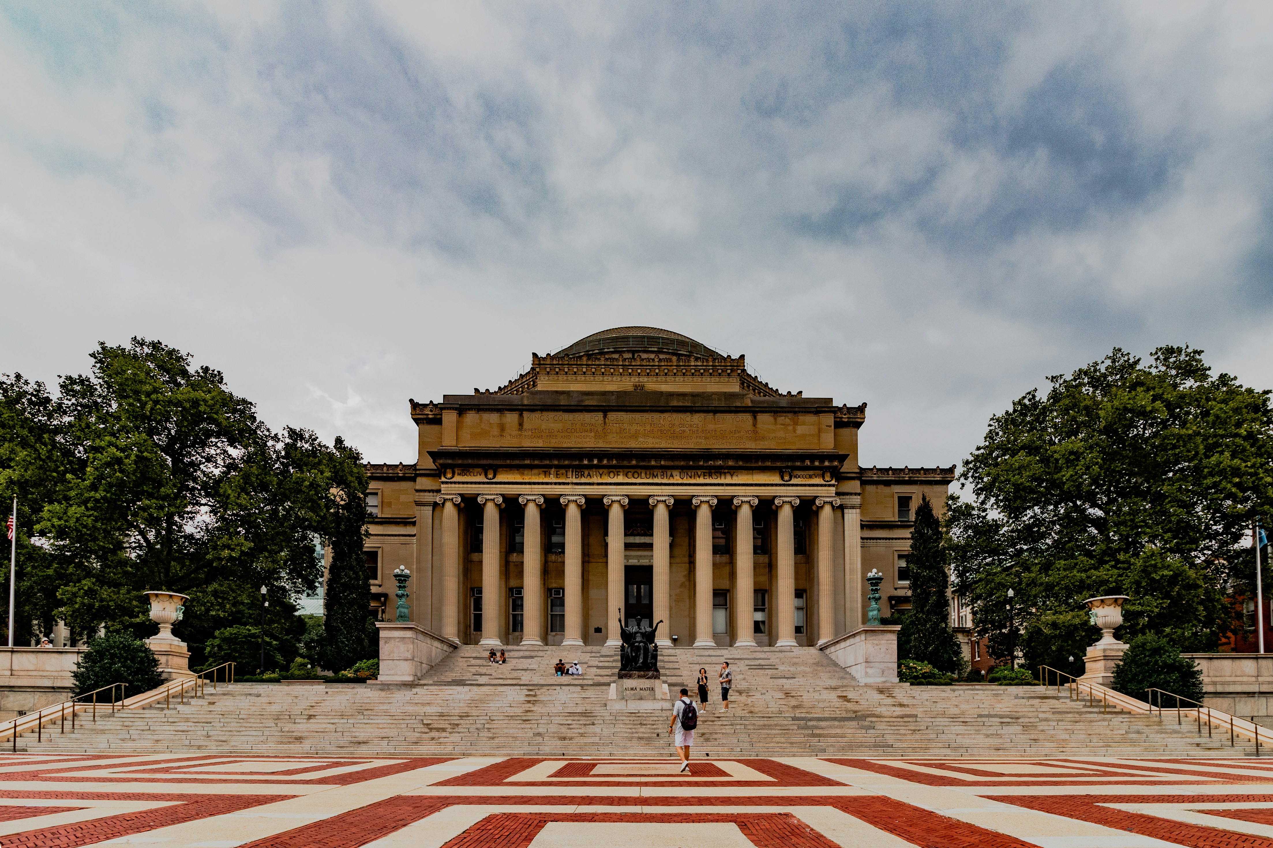 Historic building with tall columns framed by trees, set against a dramatic cloudy sky.