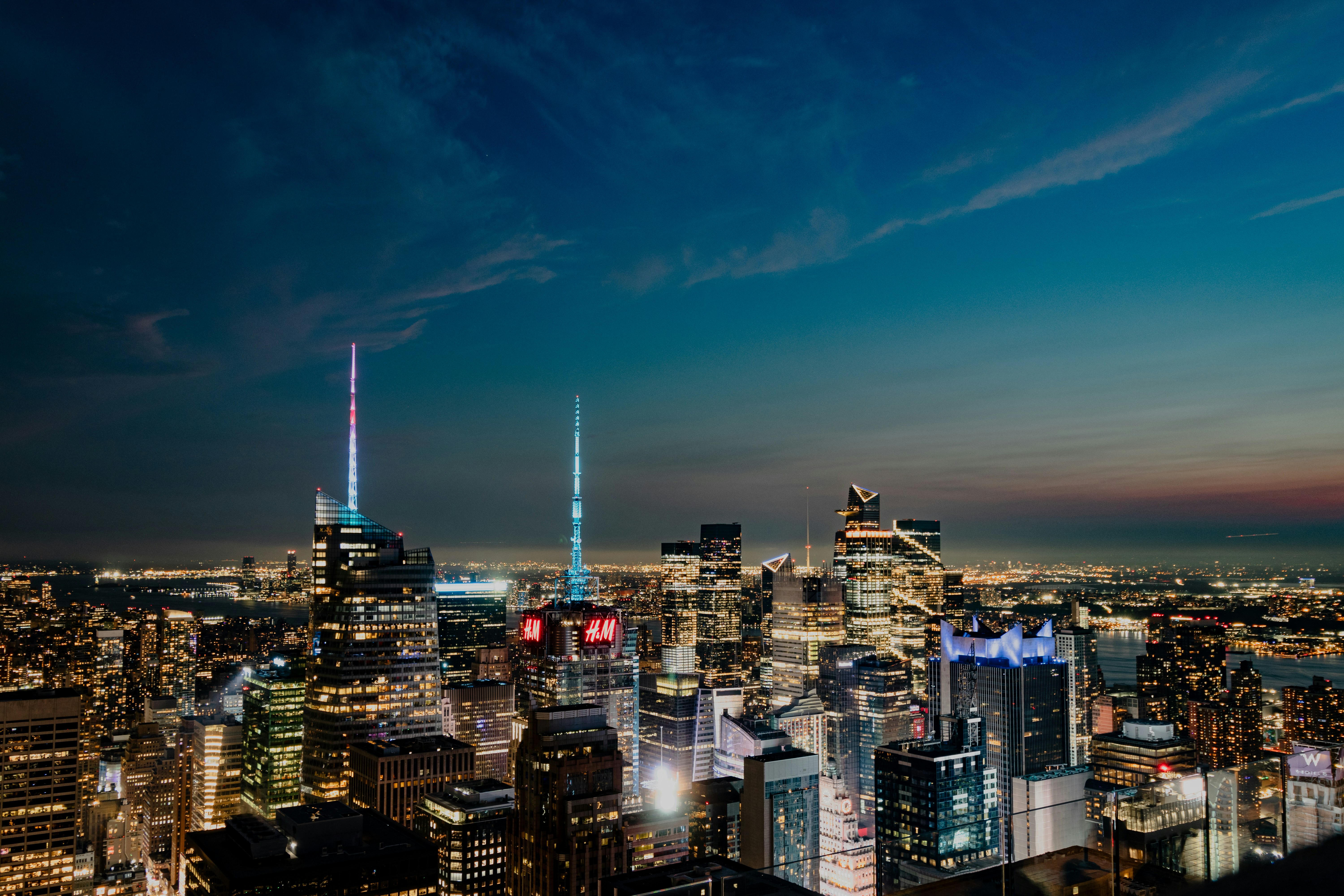 Vibrant cityscape illuminated under twilight with skyscrapers showcasing colorful lights against a deep blue sky.