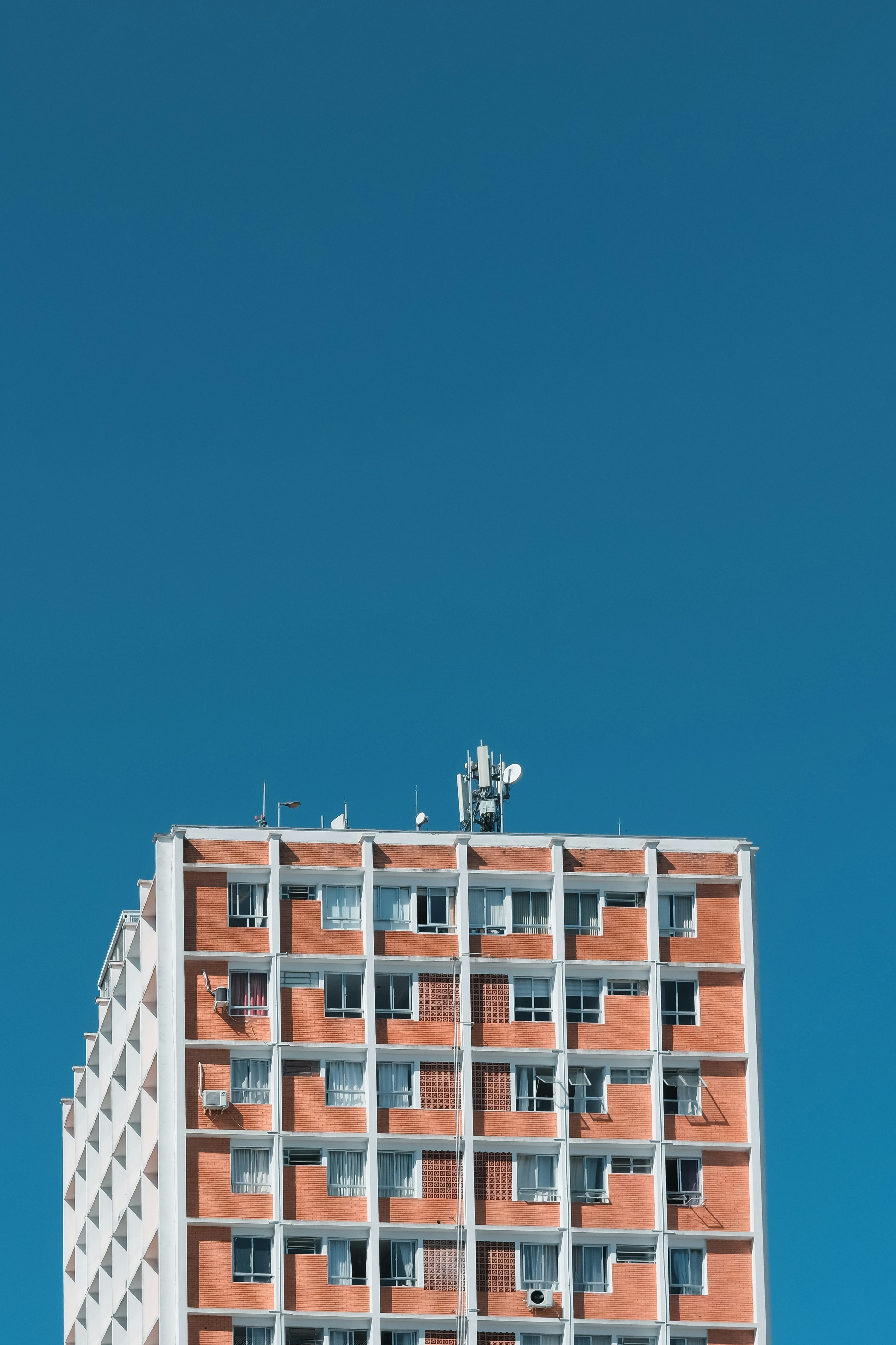 Modern residential building with a grid-like facade and telecommunications antenna, set against a vibrant blue sky.