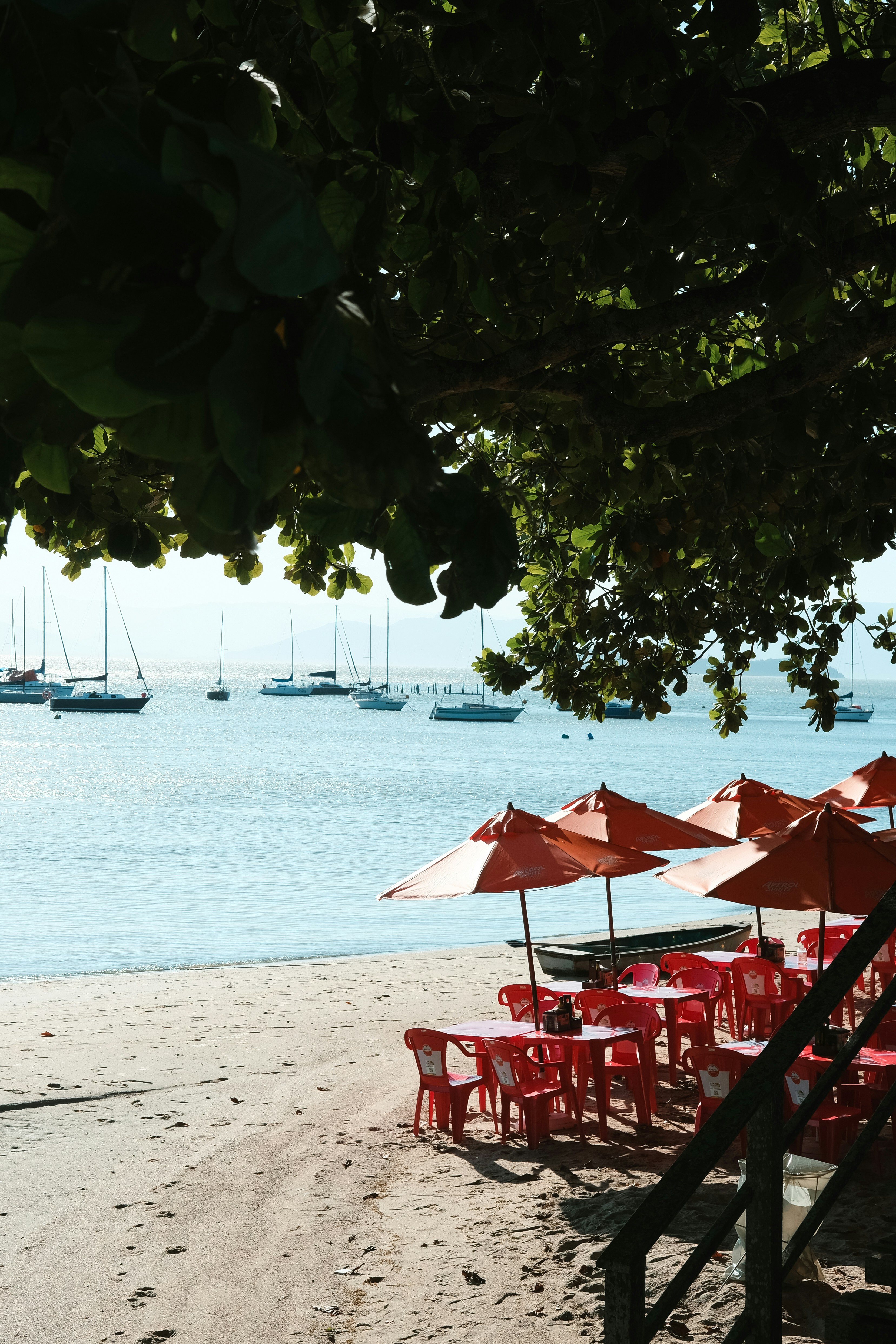 Red Terrace by the Tides: Umbrellas, Chairs, and Sailboats on a Quiet Beach