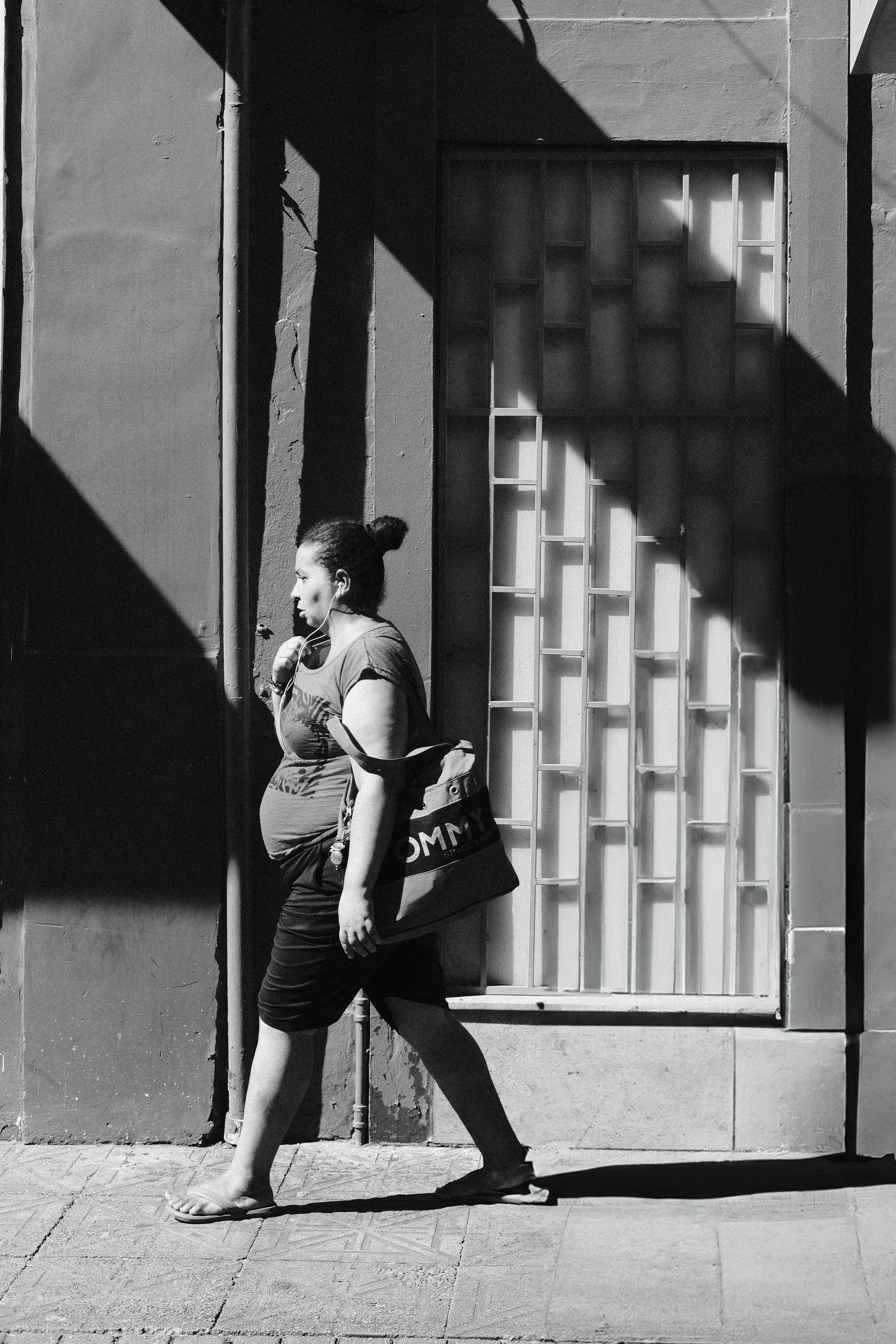 Shadowed Geometry: A Pregnant Figure Traverses a Gridded Facade
