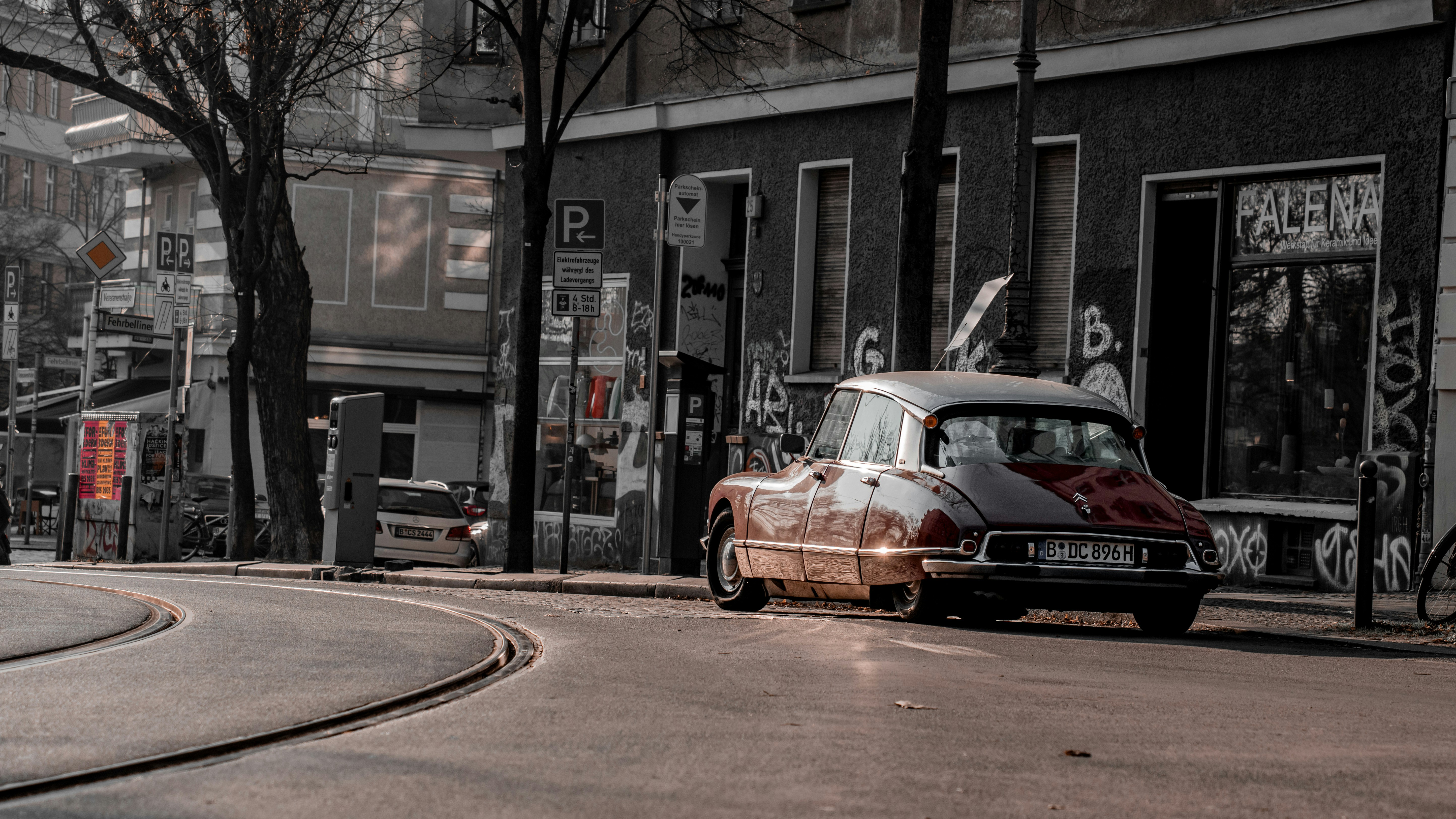 Classic car parked on a graffiti-covered street corner under soft sunlight.