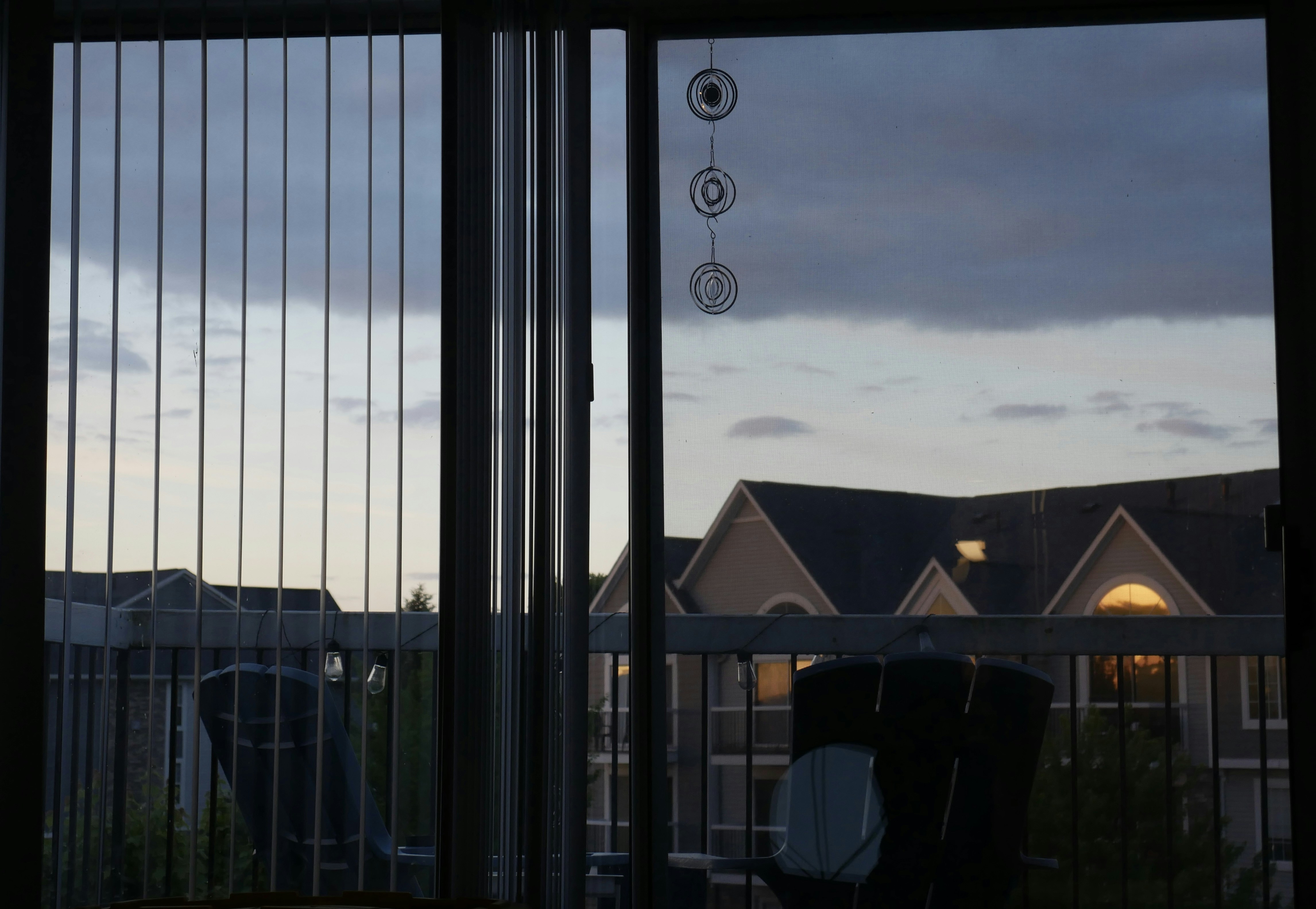 Twilight Through Balcony Glass: Three Hanging Orbs Framing a Quiet Suburban Dusk