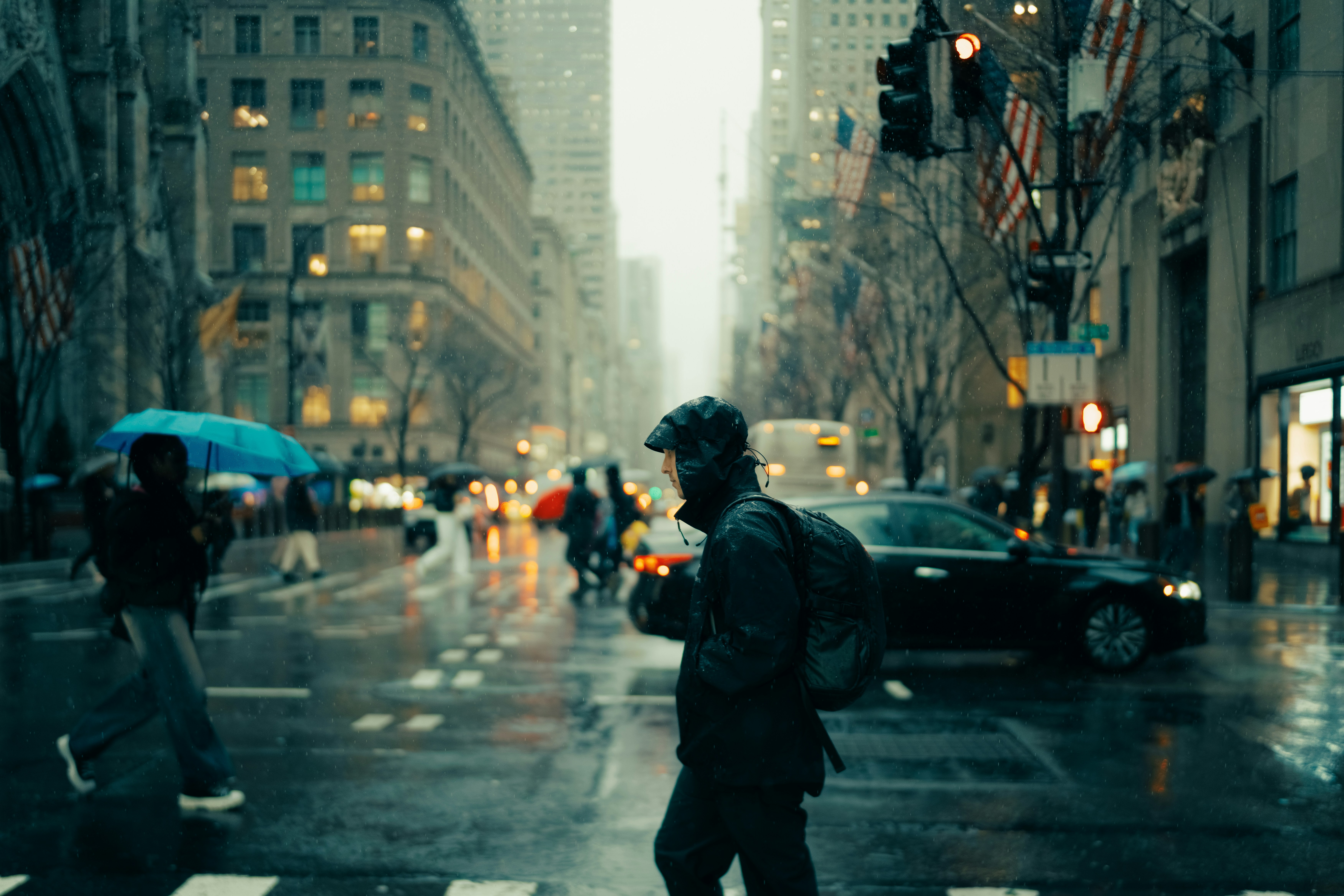 Pedestrian crossing a rainy city street amid blurred cars and colorful umbrellas, with reflections shimmering on wet pavement.