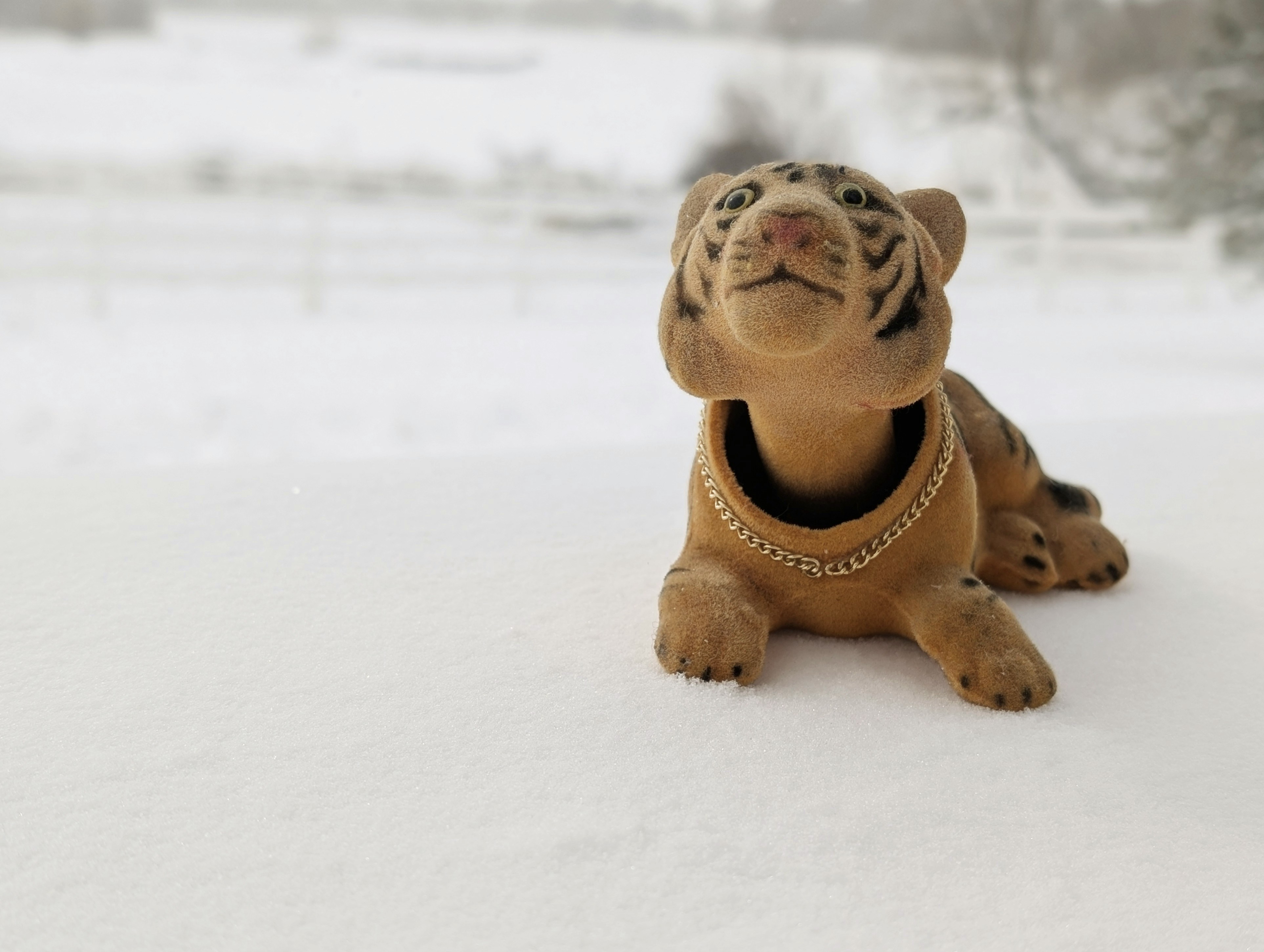 A little tiger bobblehead stuck in the middle of a blizzard. | A small toy tiger sitting in the snow