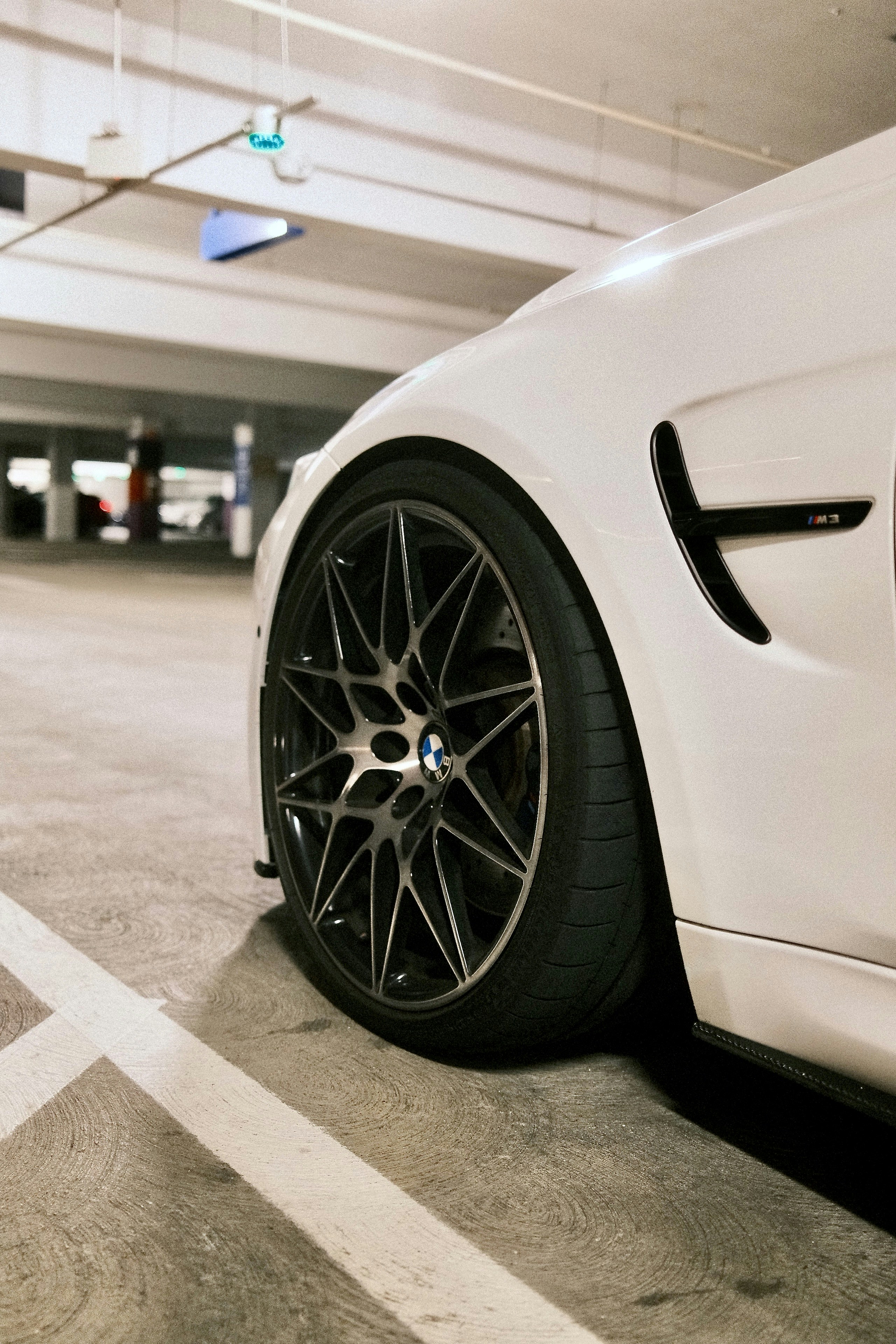 Spoked Precision: White BMW Wheel Anchored in a Quiet Parking Garage