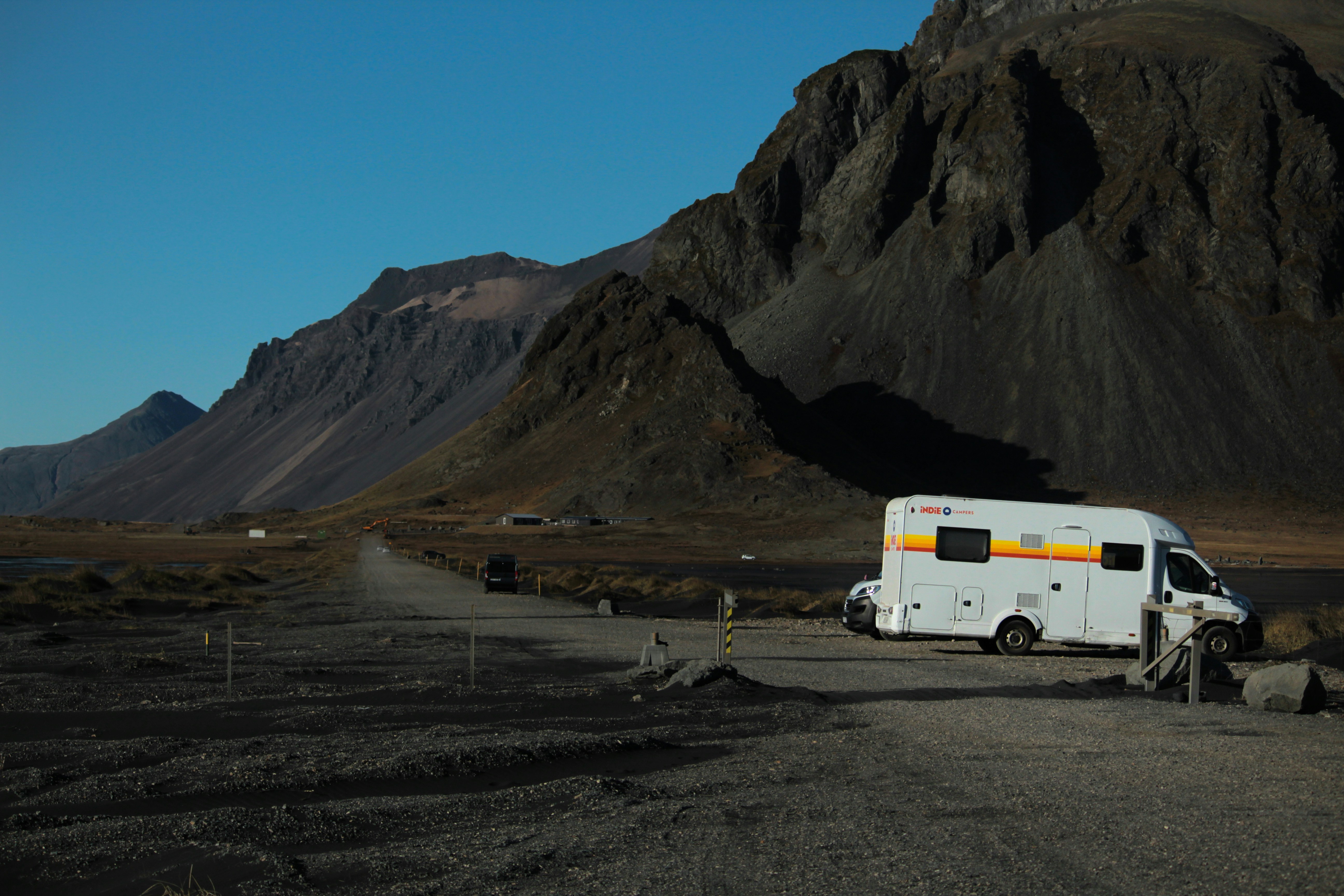 Campervan parked on a gravel road beside towering cliffs under a clear blue sky.