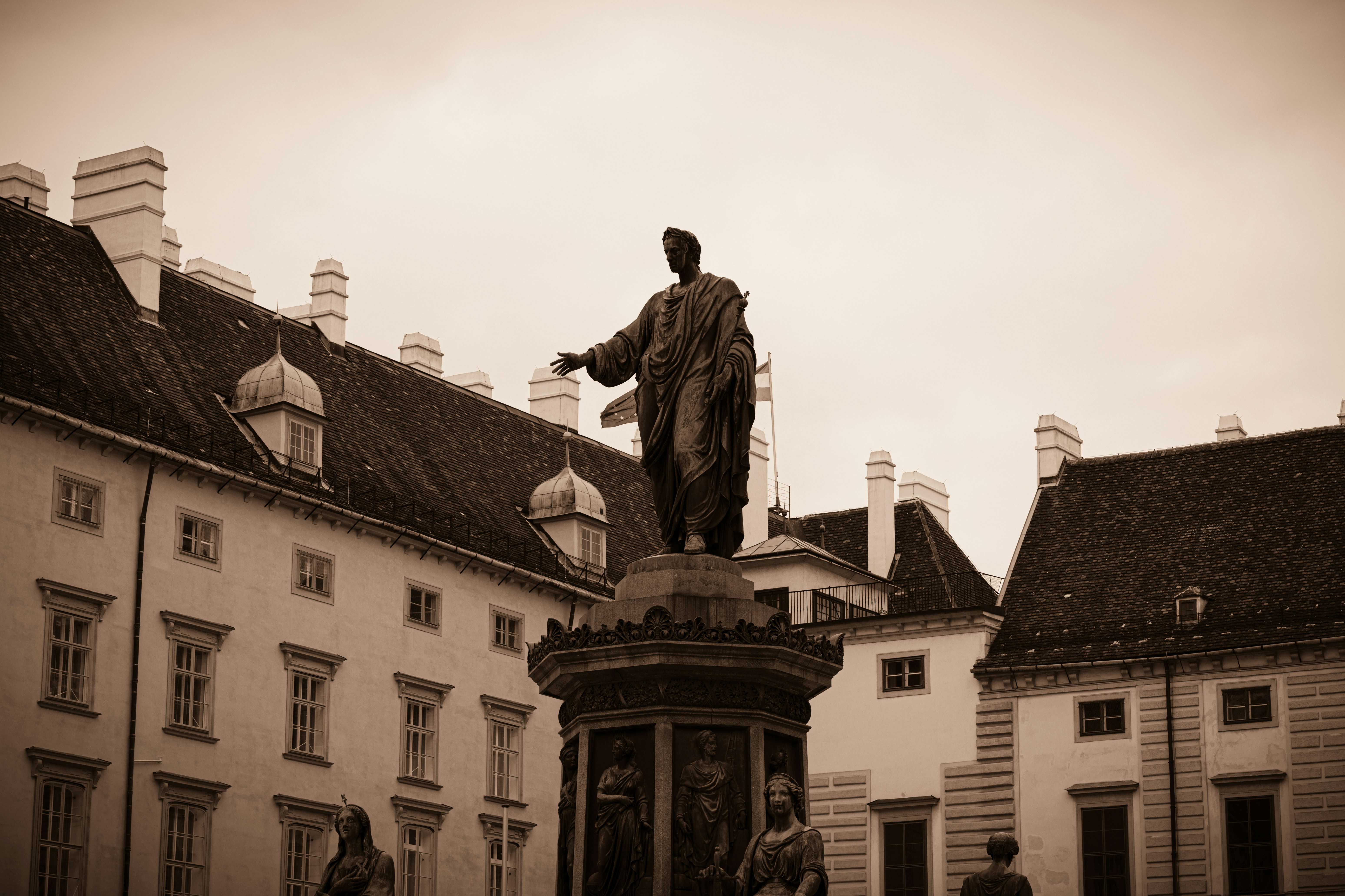 Sepia-toned statue stands against historic European architecture under a cloudy sky.