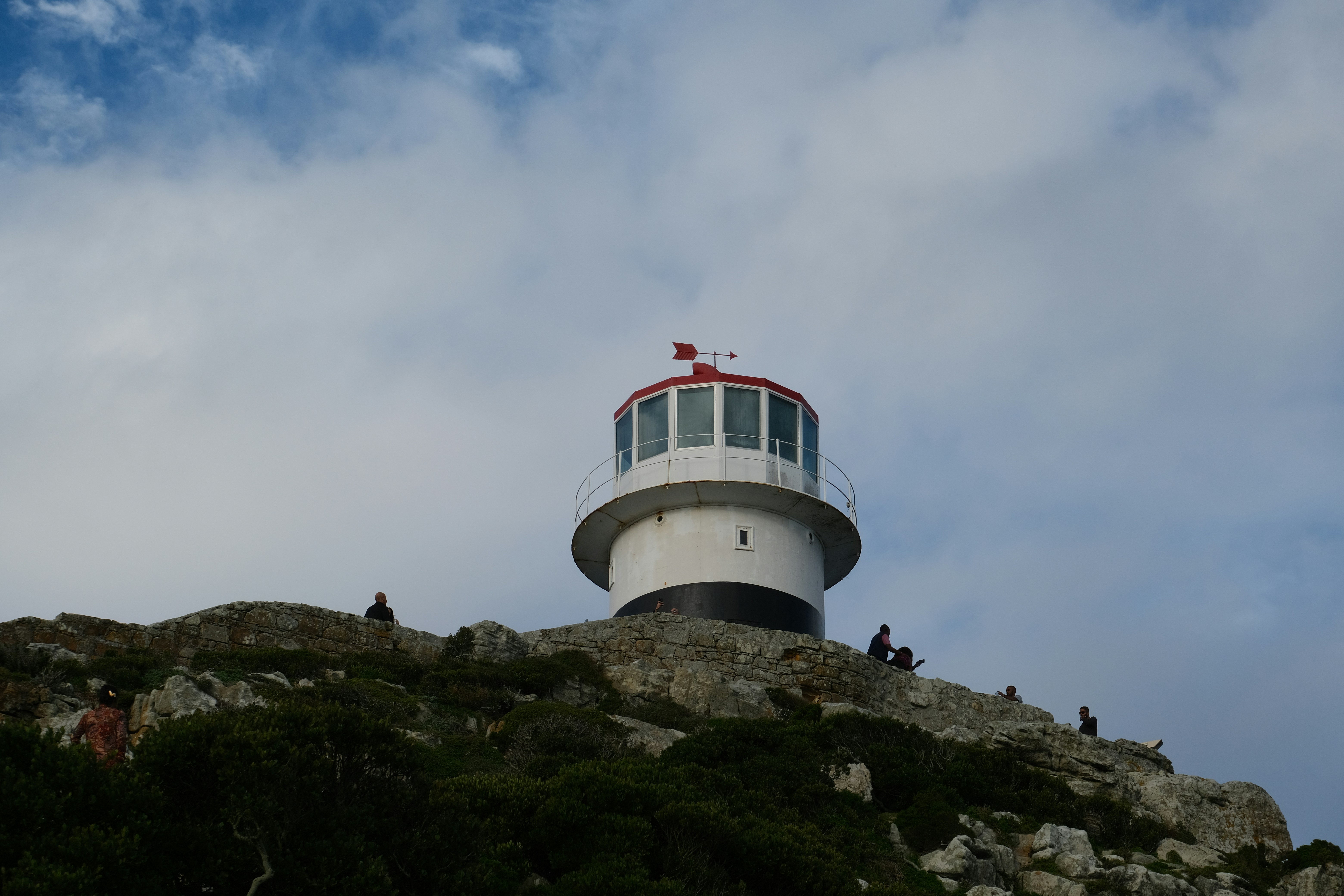 Lighthouse perched atop a rocky hill under a cloudy sky.