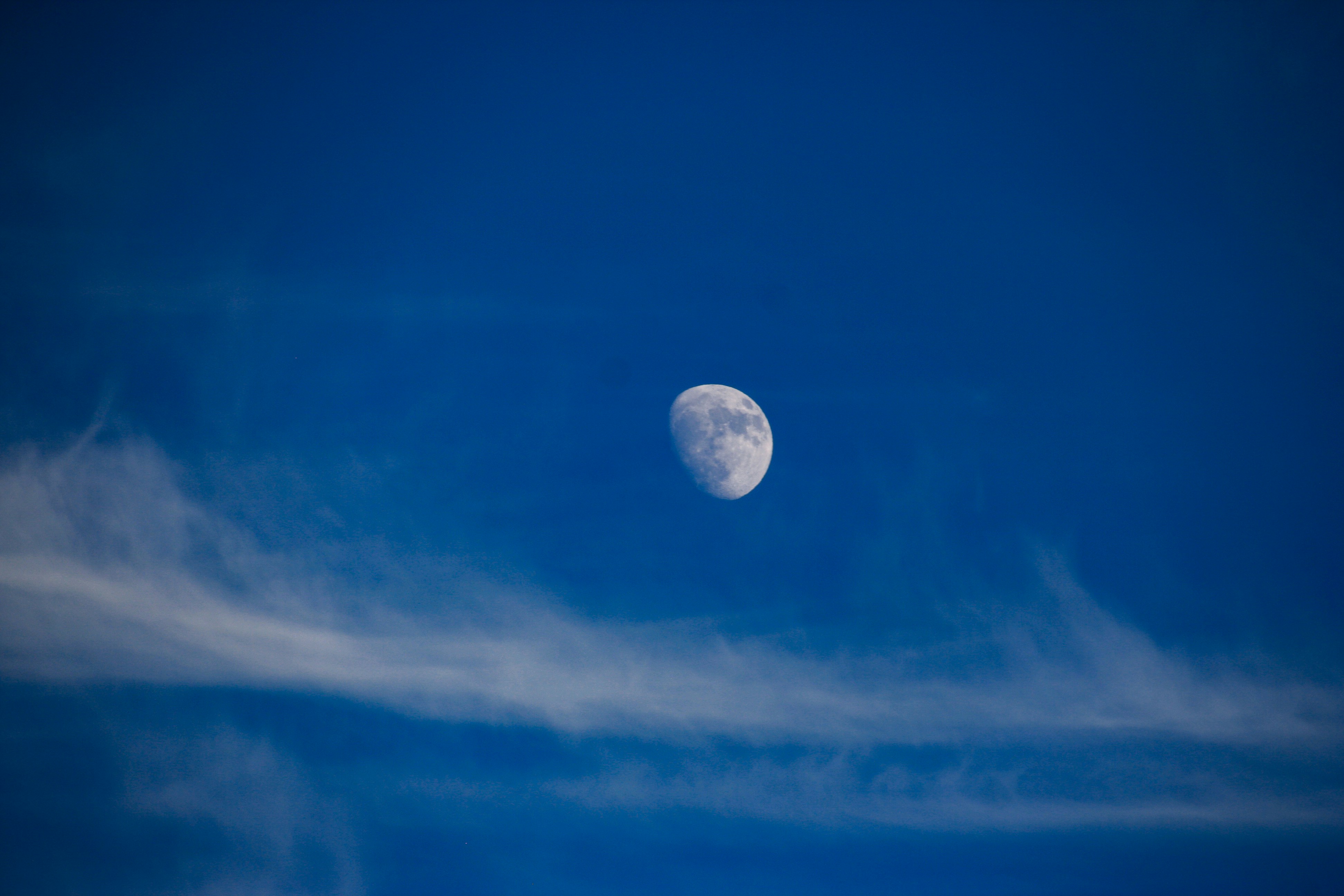 Half moon glowing against a deep blue sky with wispy clouds.
