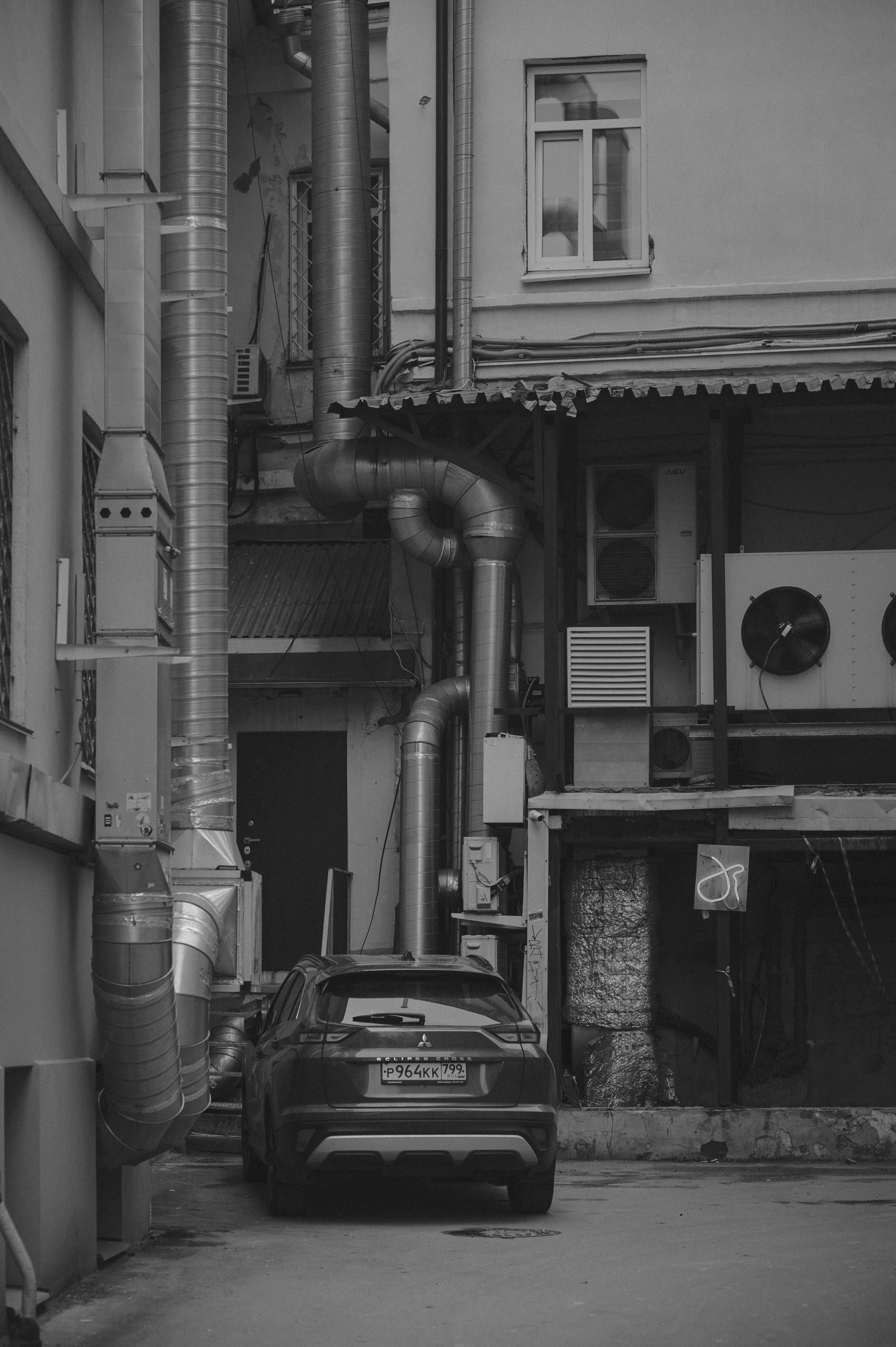 Industrial Quiet: Car Nestled Between Ductwork and Concrete