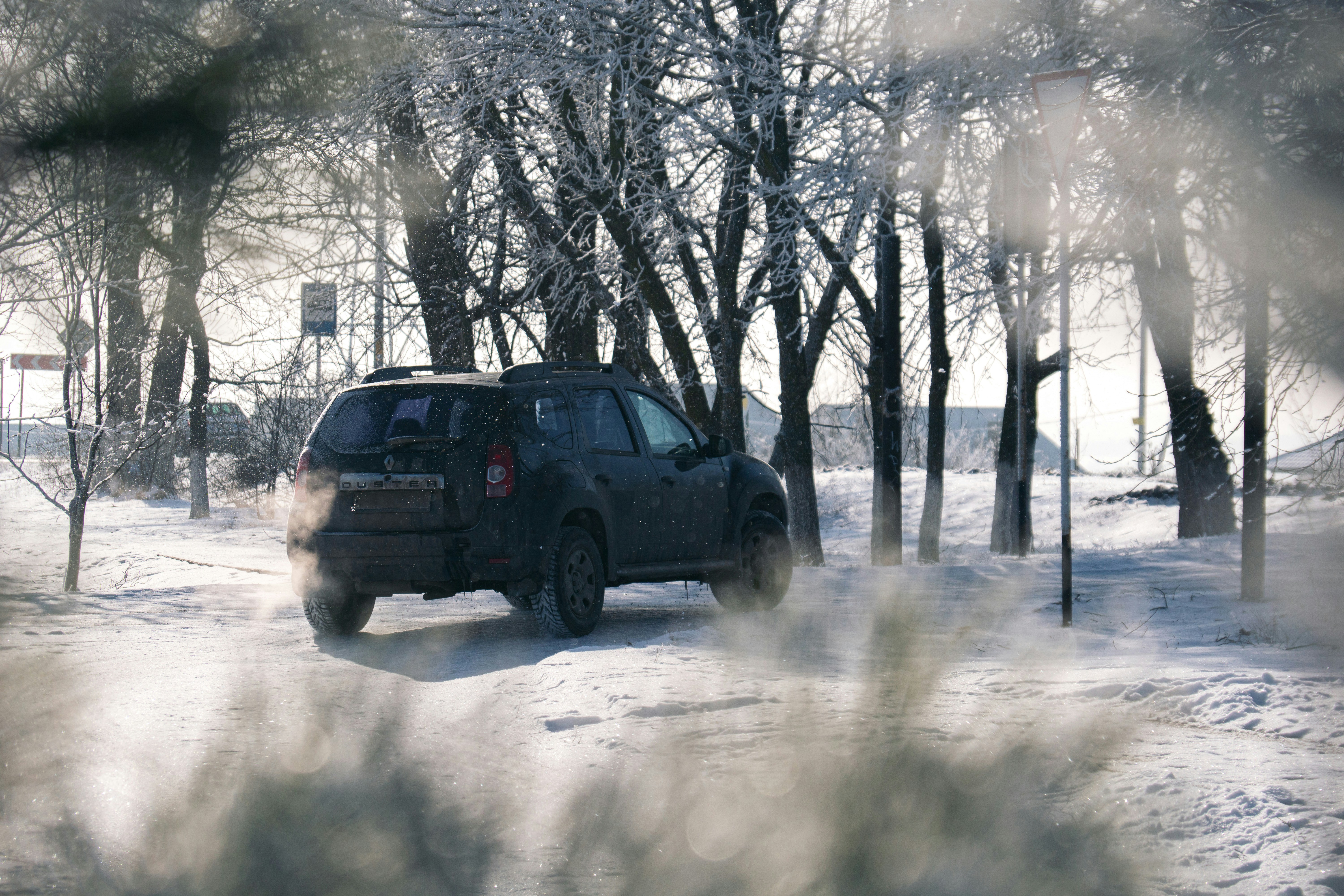 Black SUV traversing a snow-covered road flanked by bare trees.