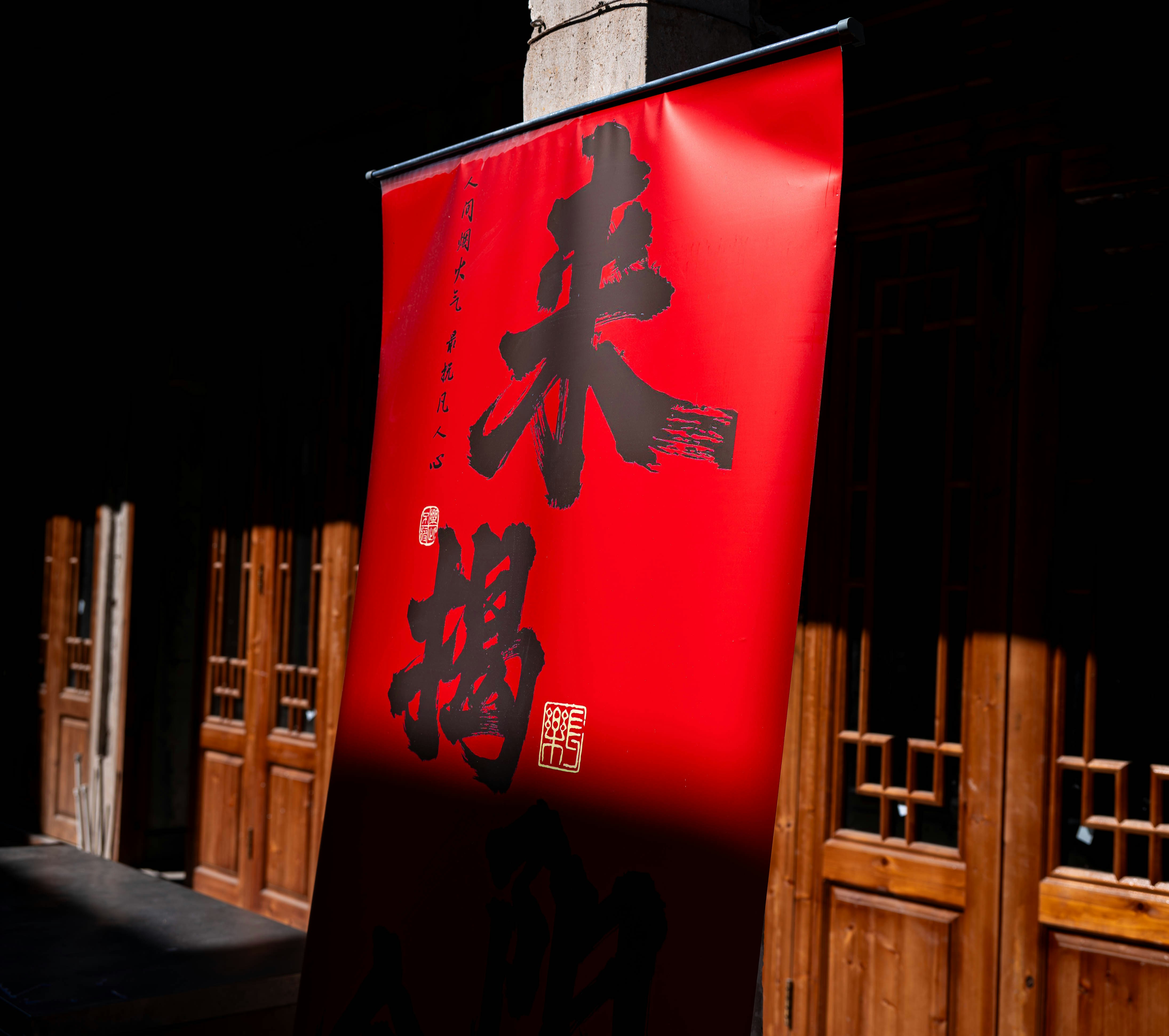 Red banner with bold black Chinese characters in a shadowed, sunlit alley.