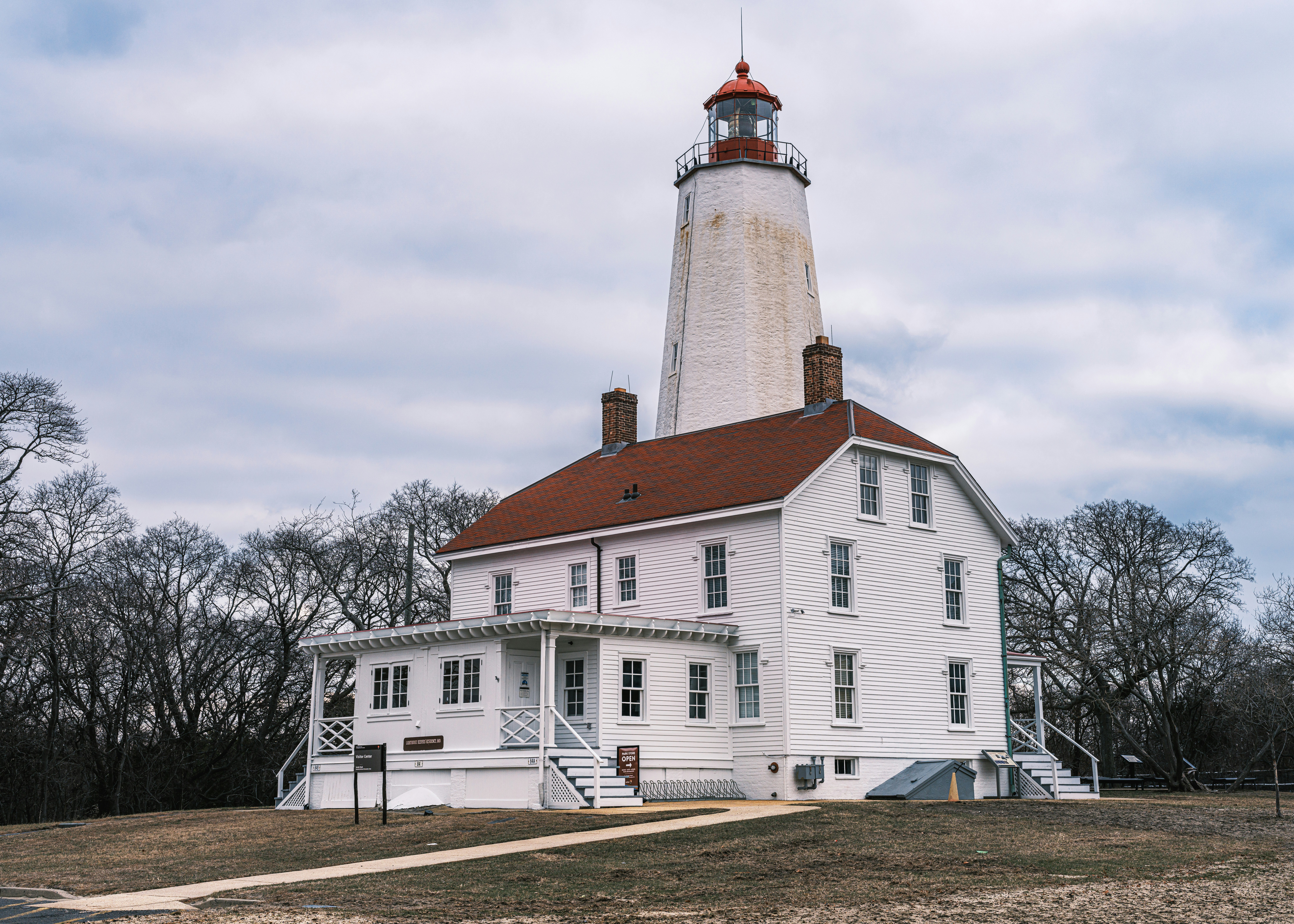 Historic Sandy Hook Lighthouse with bare trees under a cloudy winter sky.