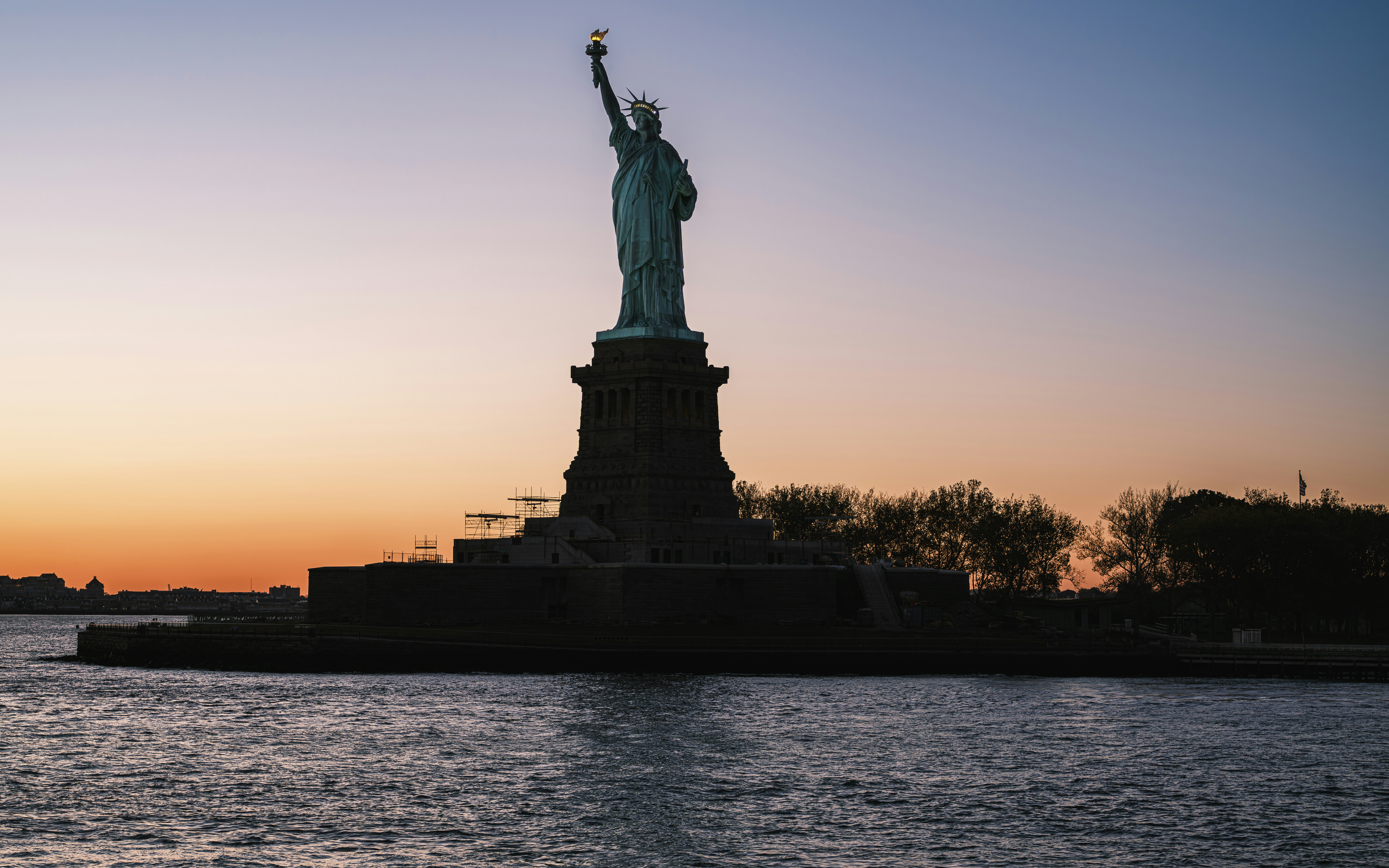 Silhouette of the Statue of Liberty against a vibrant sunset on Liberty Island.