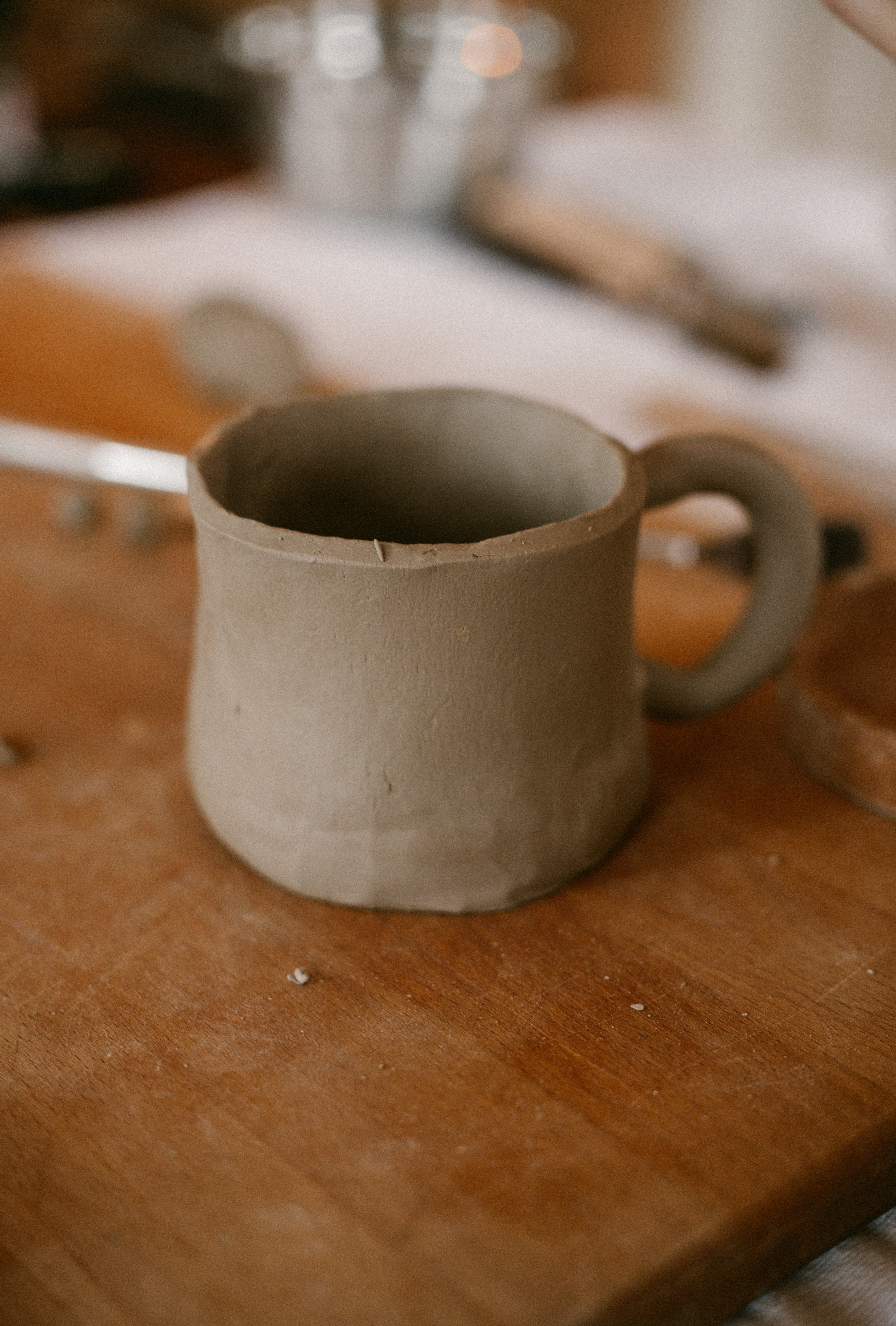 Close-up photograph of a handmade ceramic mug on a wooden worktable, with a softly blurred workshop background.