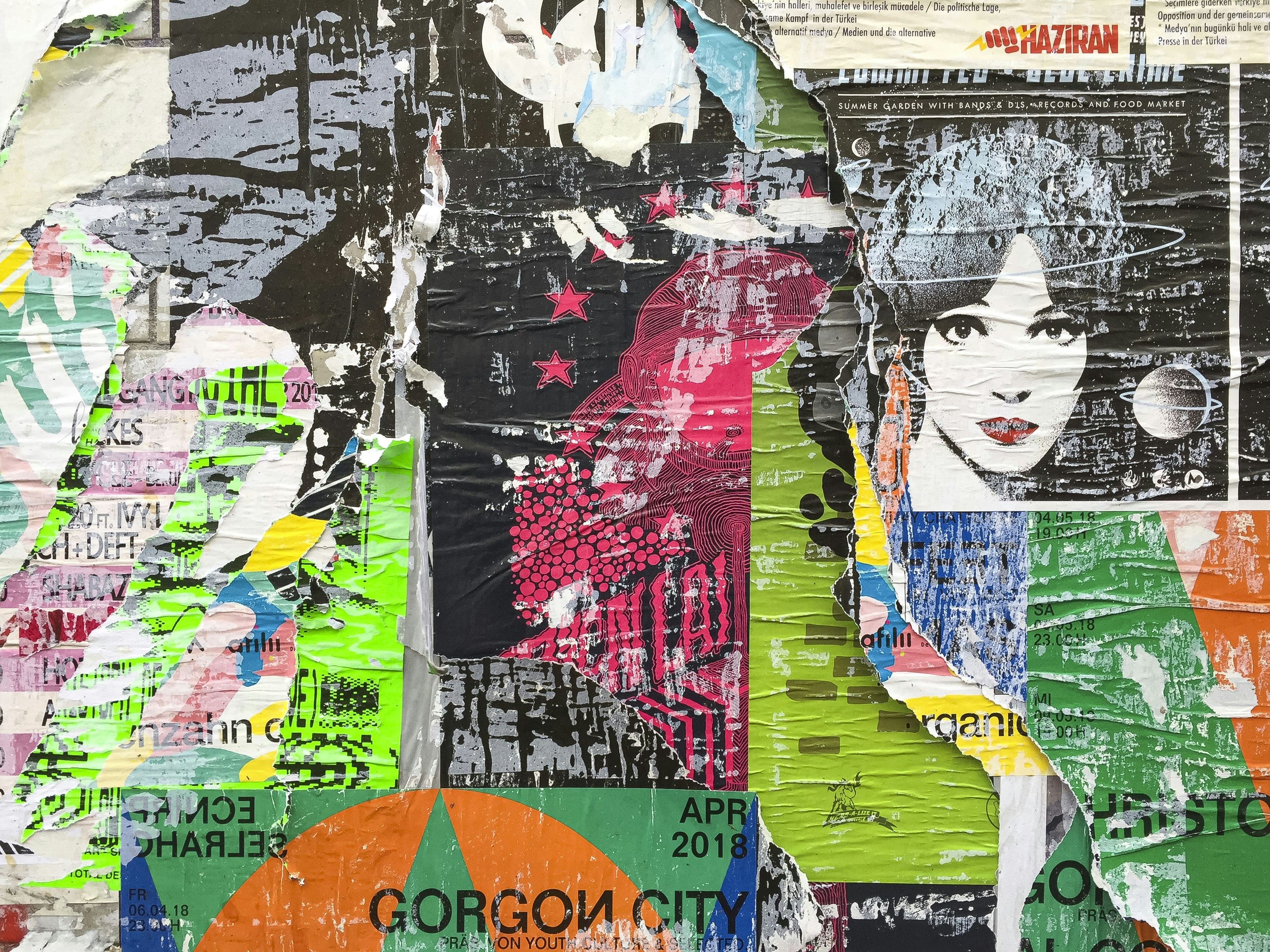Torn music and theater posters create a vibrant collage of colors and textures on a wall.