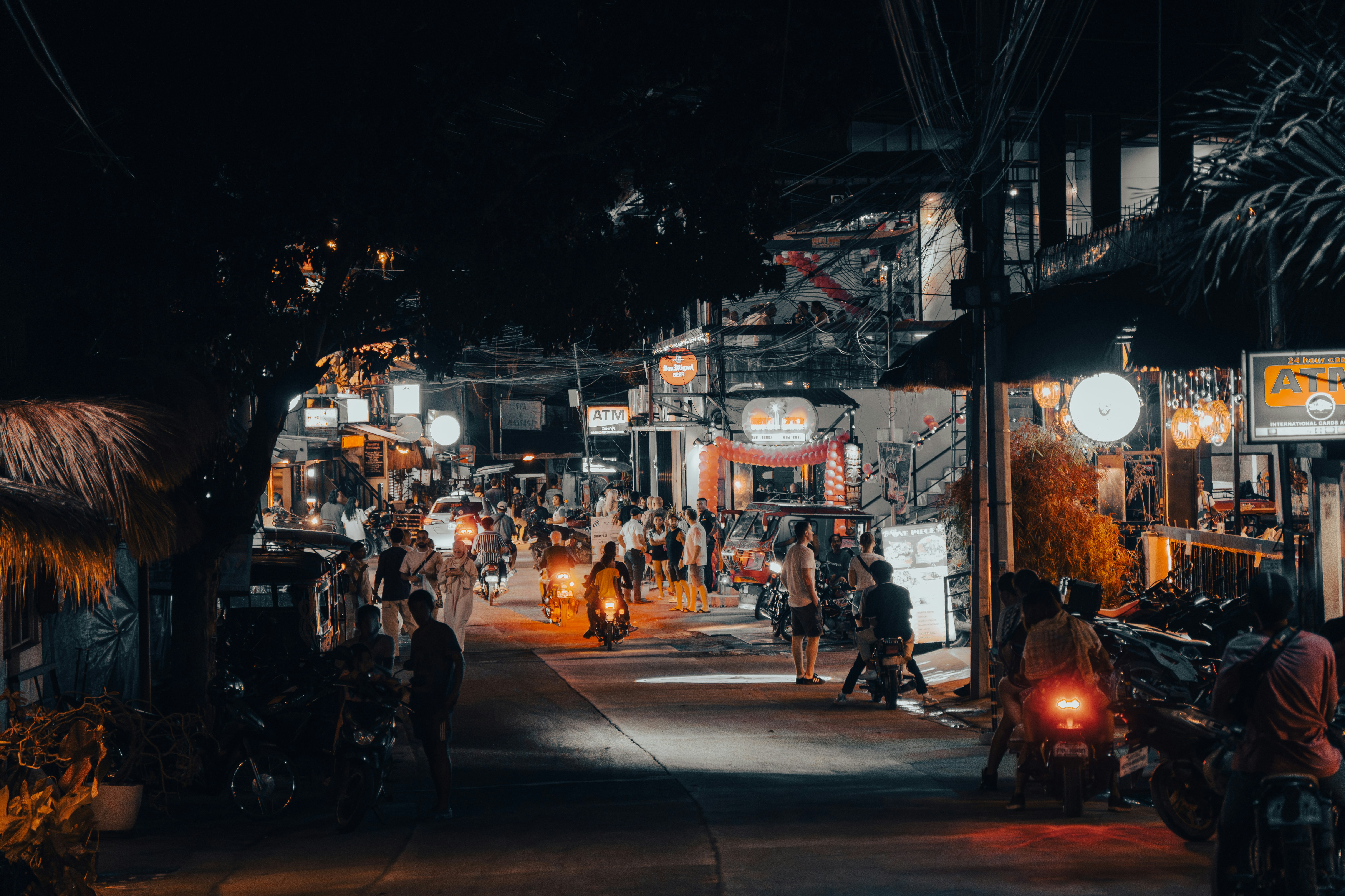 Busy street scene with people and motorcycles under warm street lights at night.