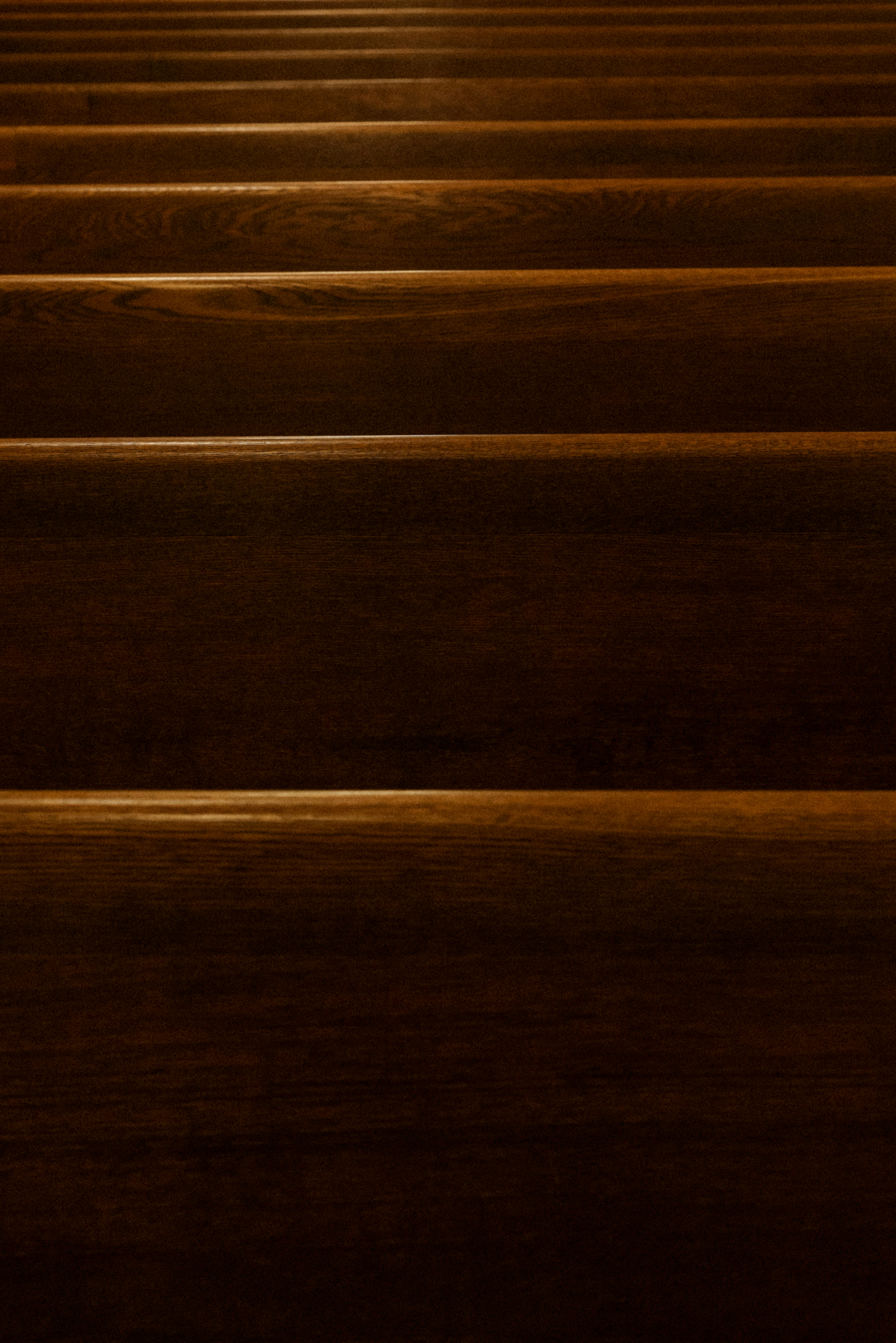 Close-up view of polished wooden stair treads, showcasing their rich texture and warm tones. The image emphasizes the interplay of light and shadow on the surface.