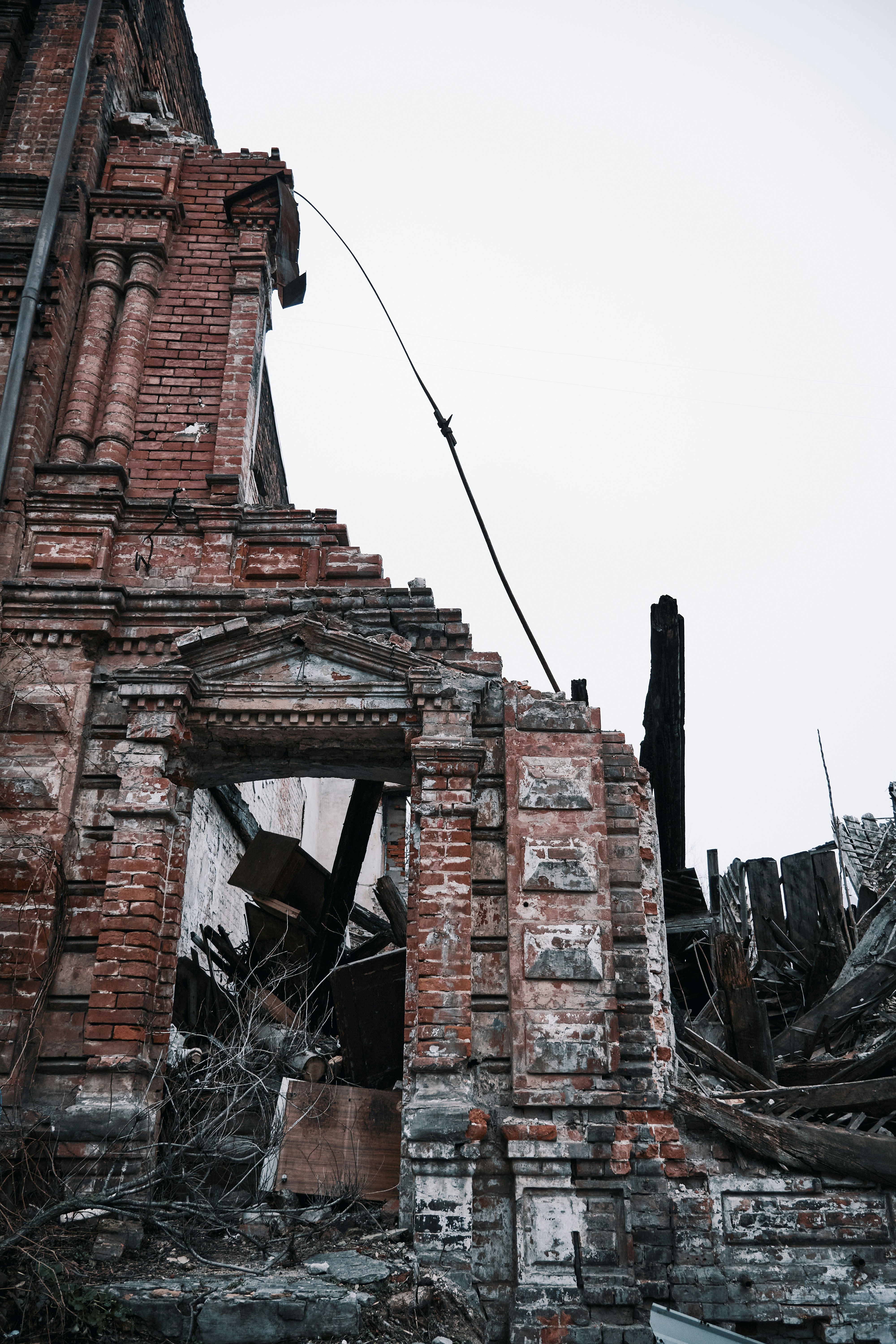 Ruined brick façade: crumbling archway and weathered debris under a stark sky
