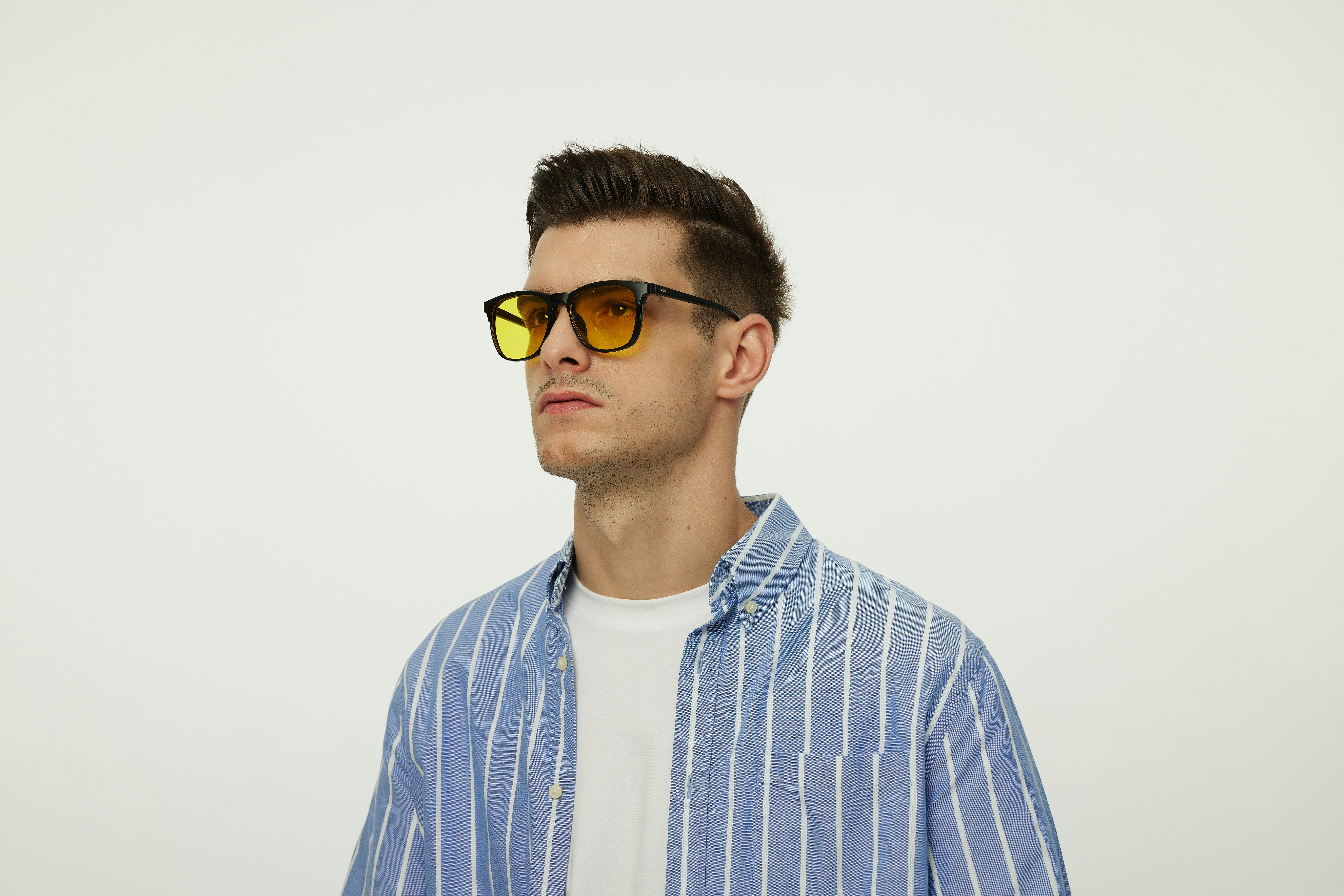 Man in striped shirt wearing black sunglasses with yellow-tinted lenses against a plain background.